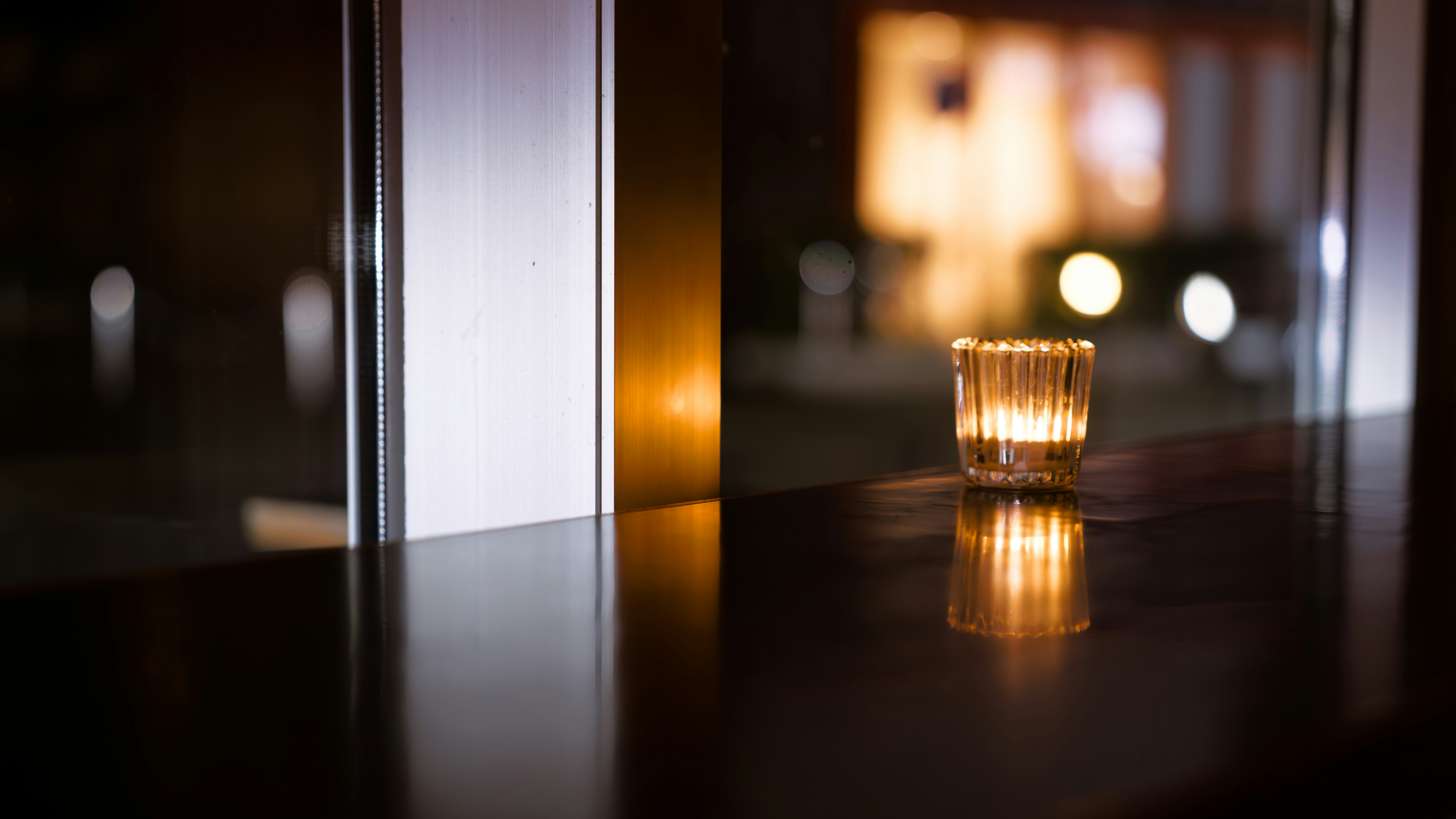 Warm solitary glow: a candle on a reflective bar