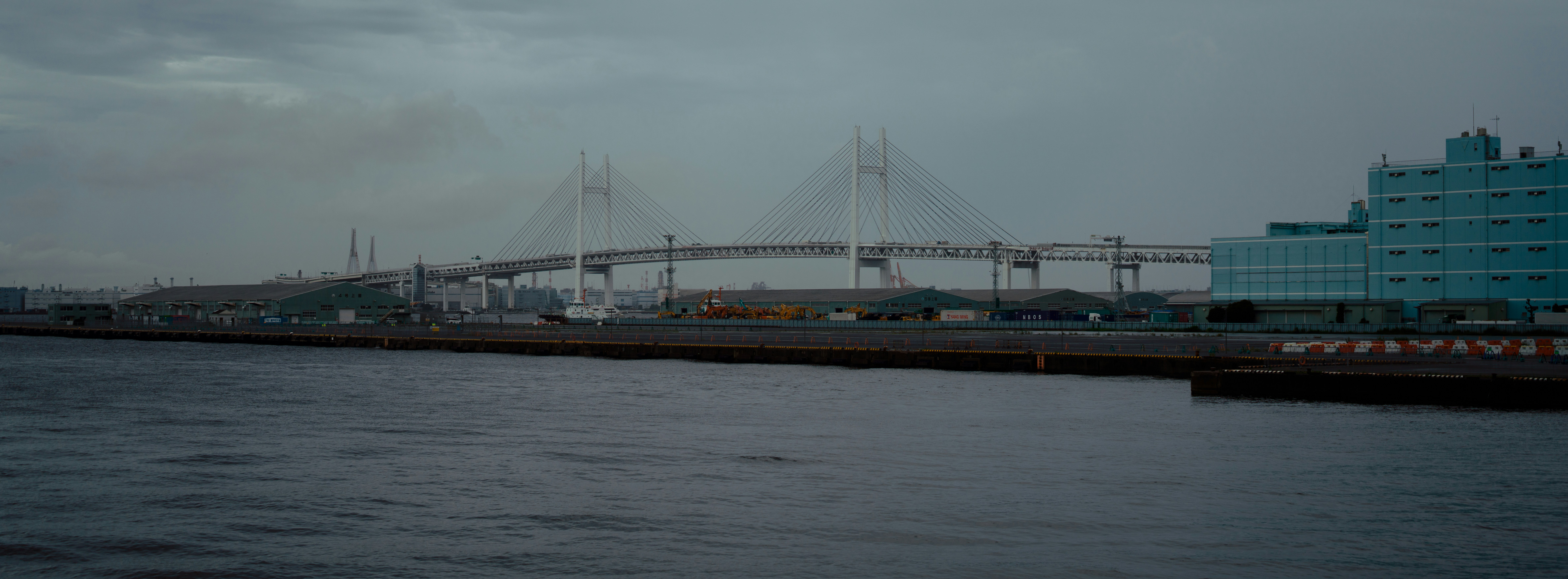 Bridge and seawall at dusk: calm waters beneath a distant skyline
