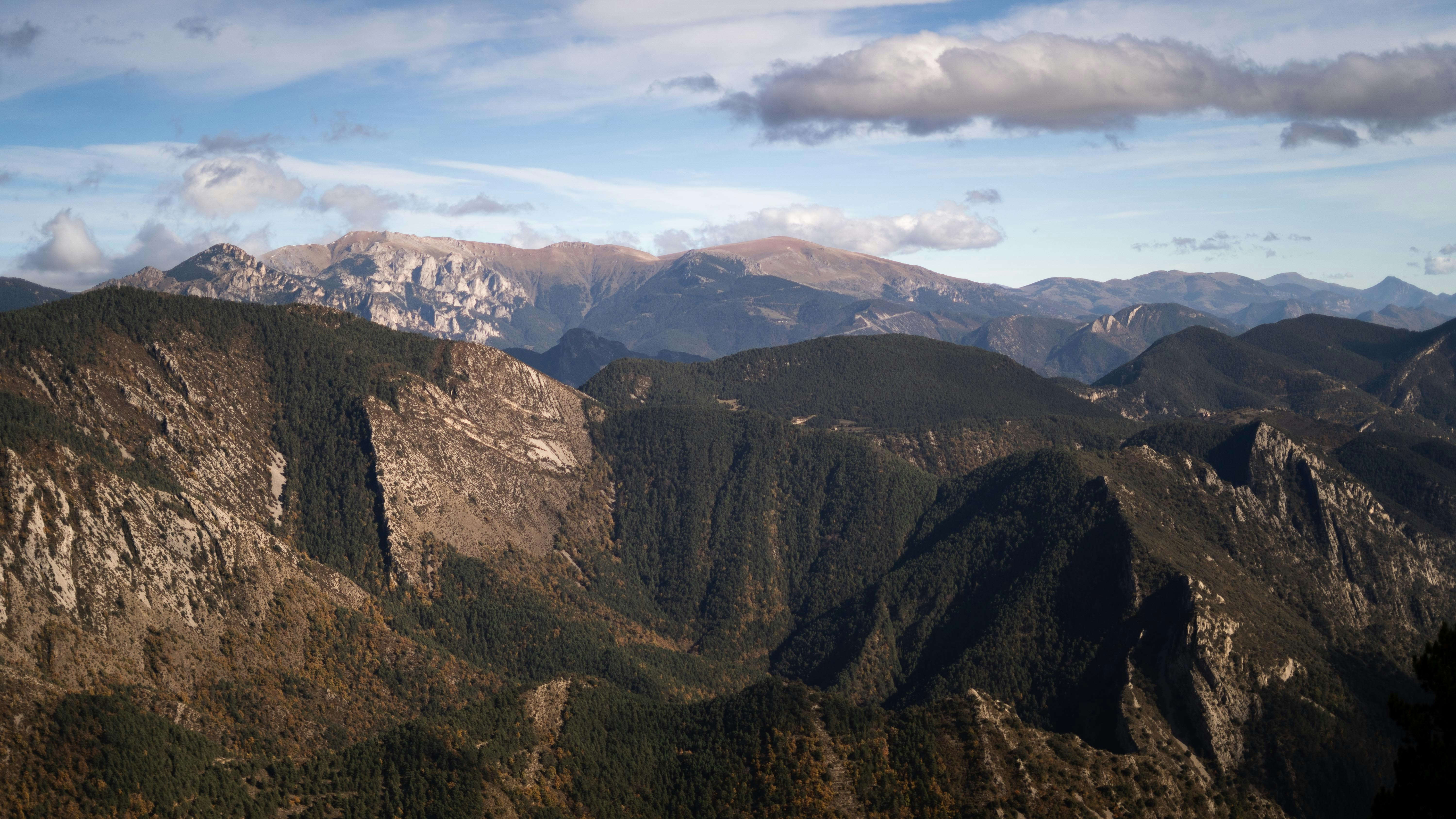 Expansive mountain ridges under a partly cloudy sky with distant peaks and a sense of depth.