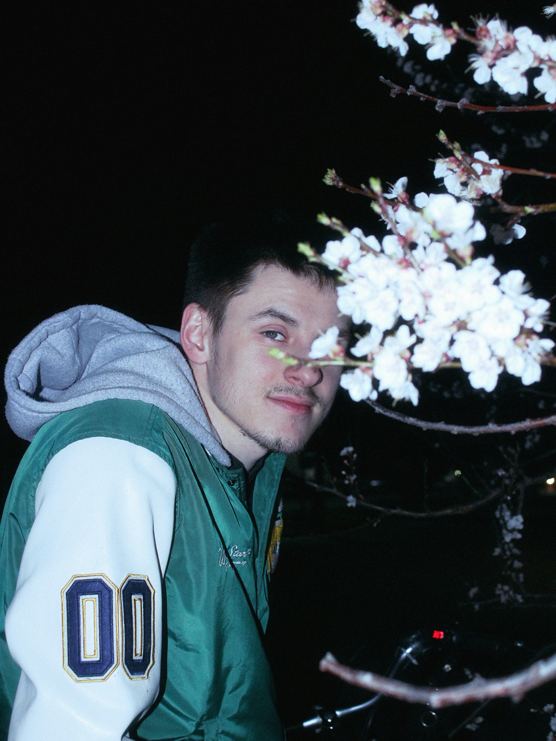 Night Bloom Portrait under Streetlight: Neon Cherry Blossoms and a Teen in Green Varsity Jacket