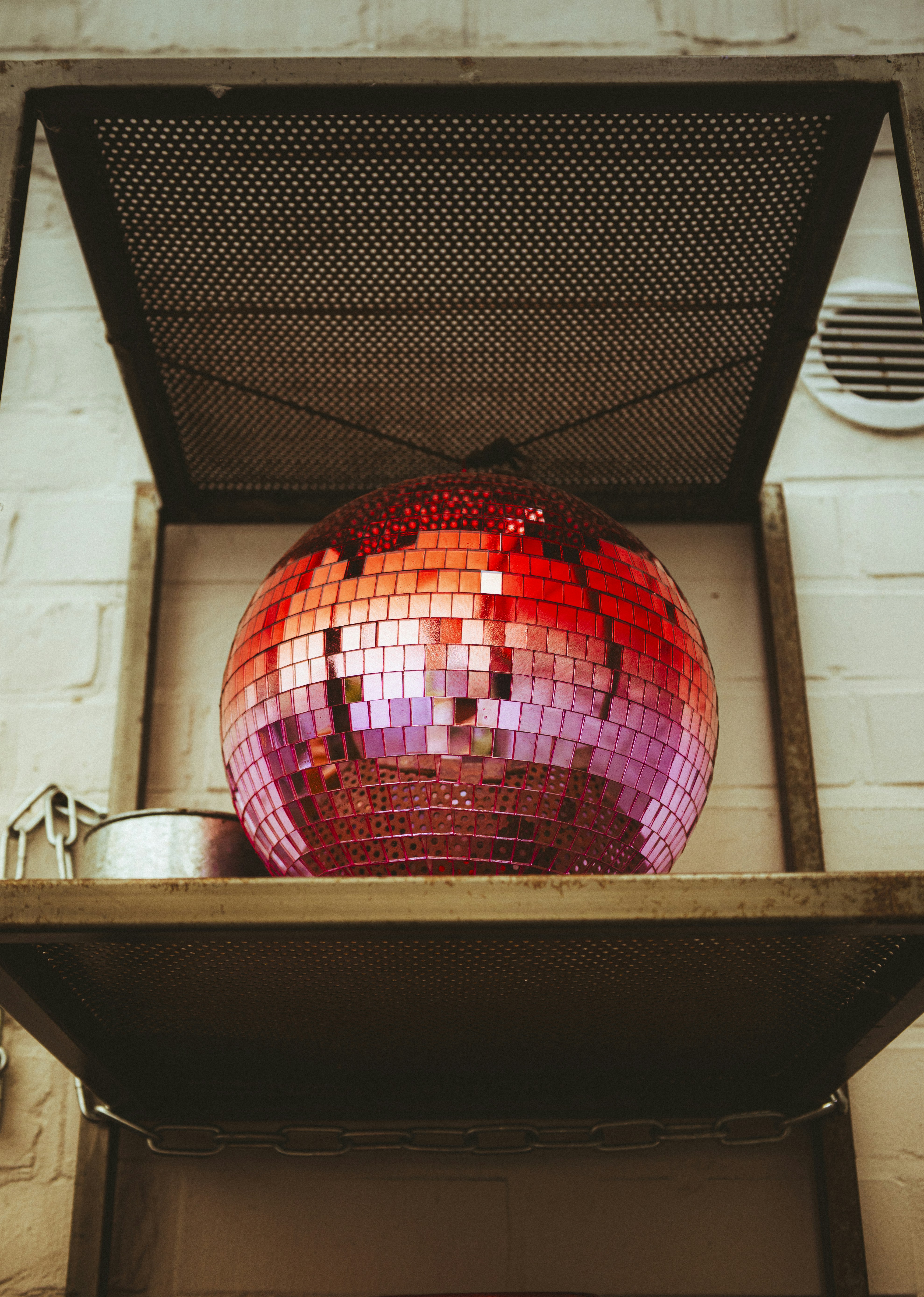 Reflective red and pink disco ball on a rustic shelf.
