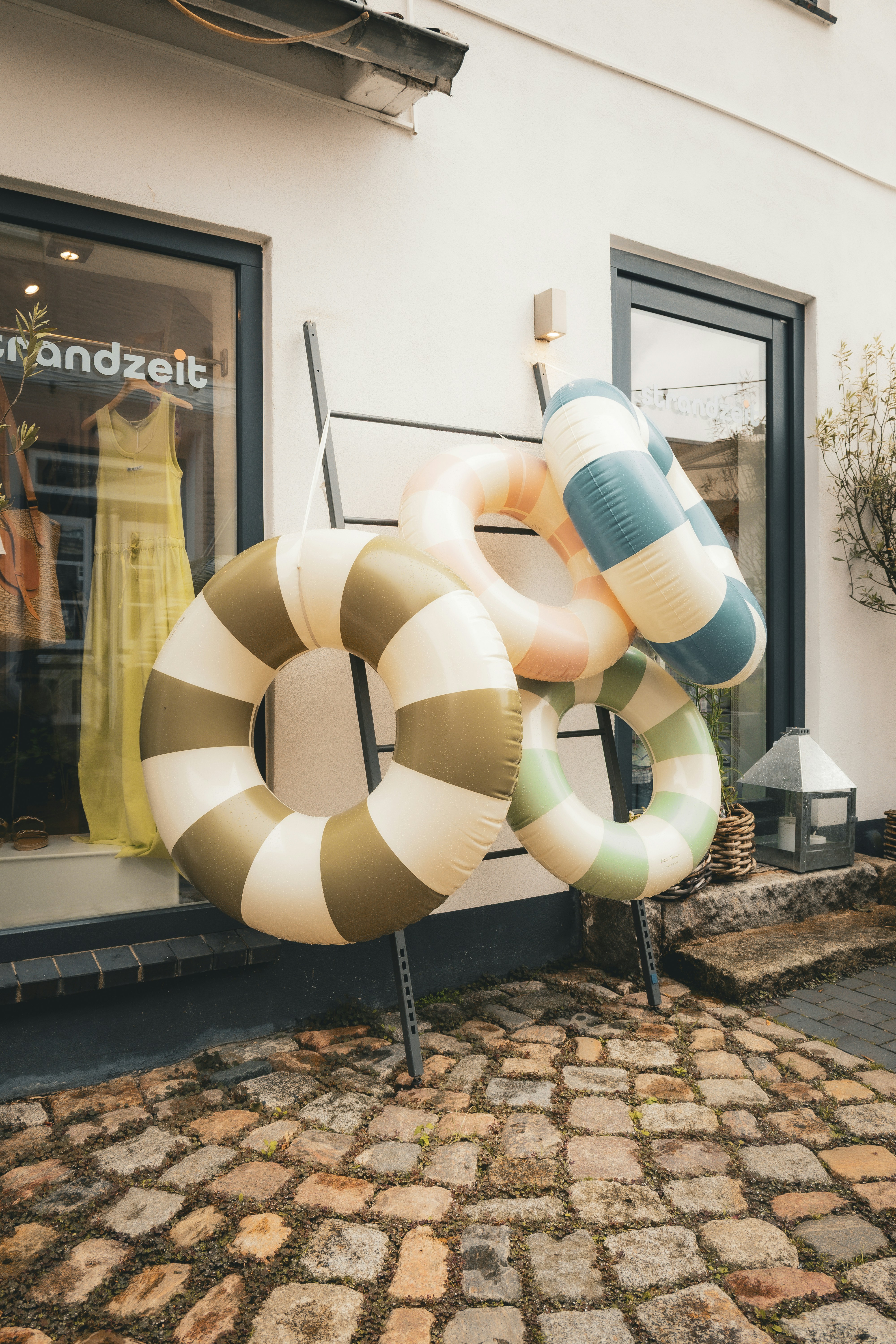 Colorful life rings lean against a sunlit storefront on a cobblestone street