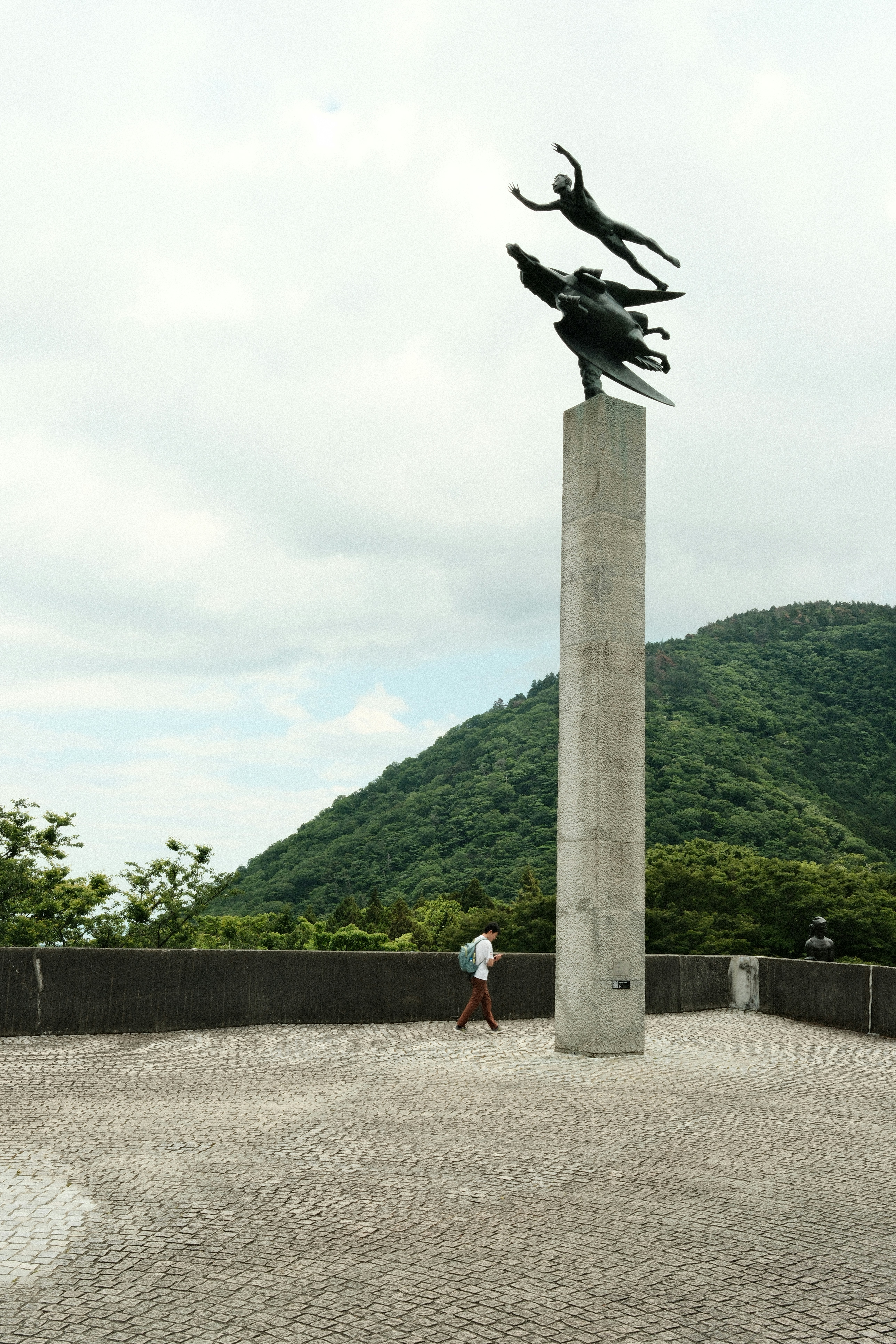 Monumental Sentinel: A Lone Visitor Beneath a Towering Sculpture