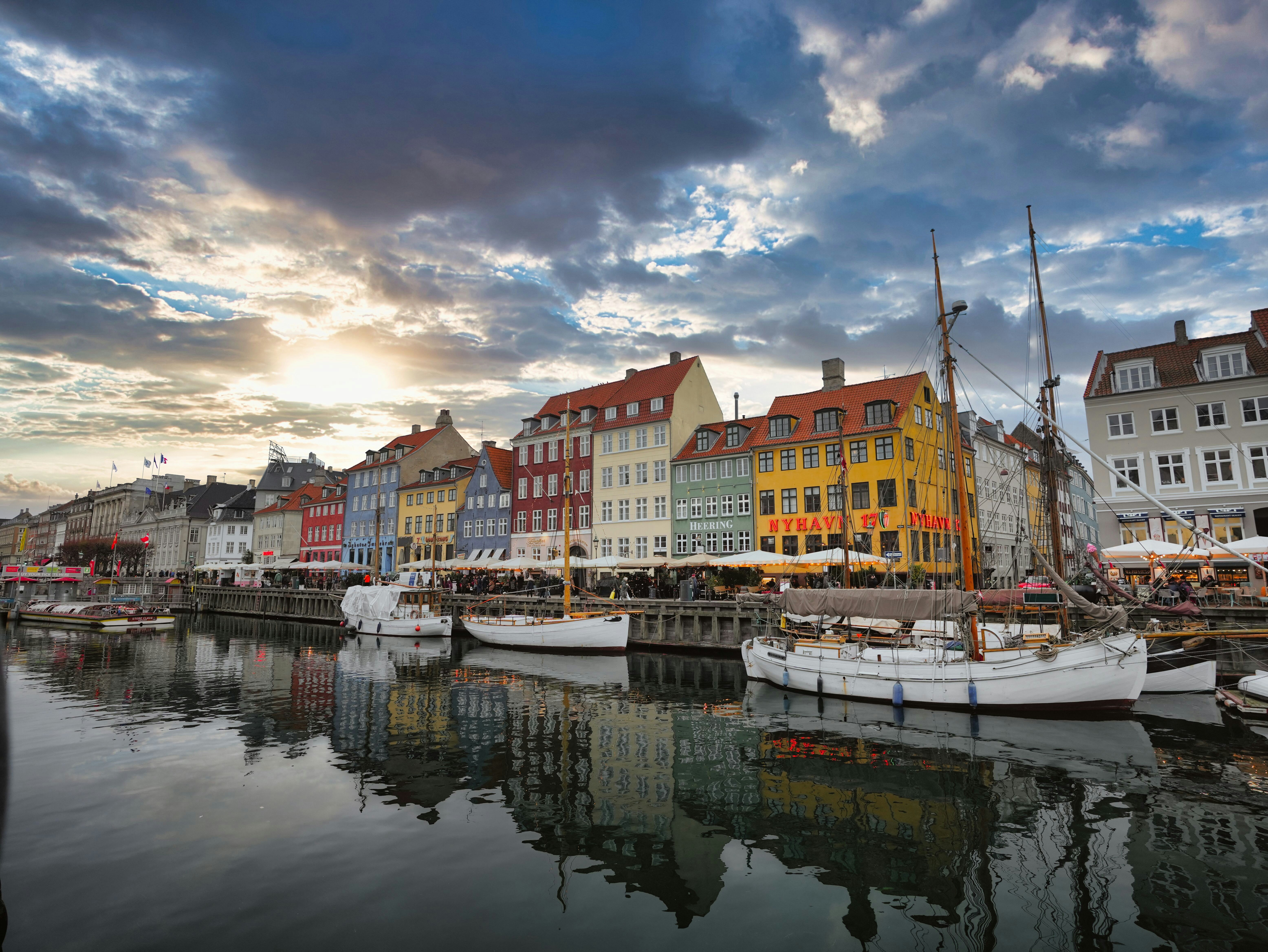 Colorful waterfront houses line Nyhavn with boats docked along calm canal, sunlight catching the facades and reflections in the water.