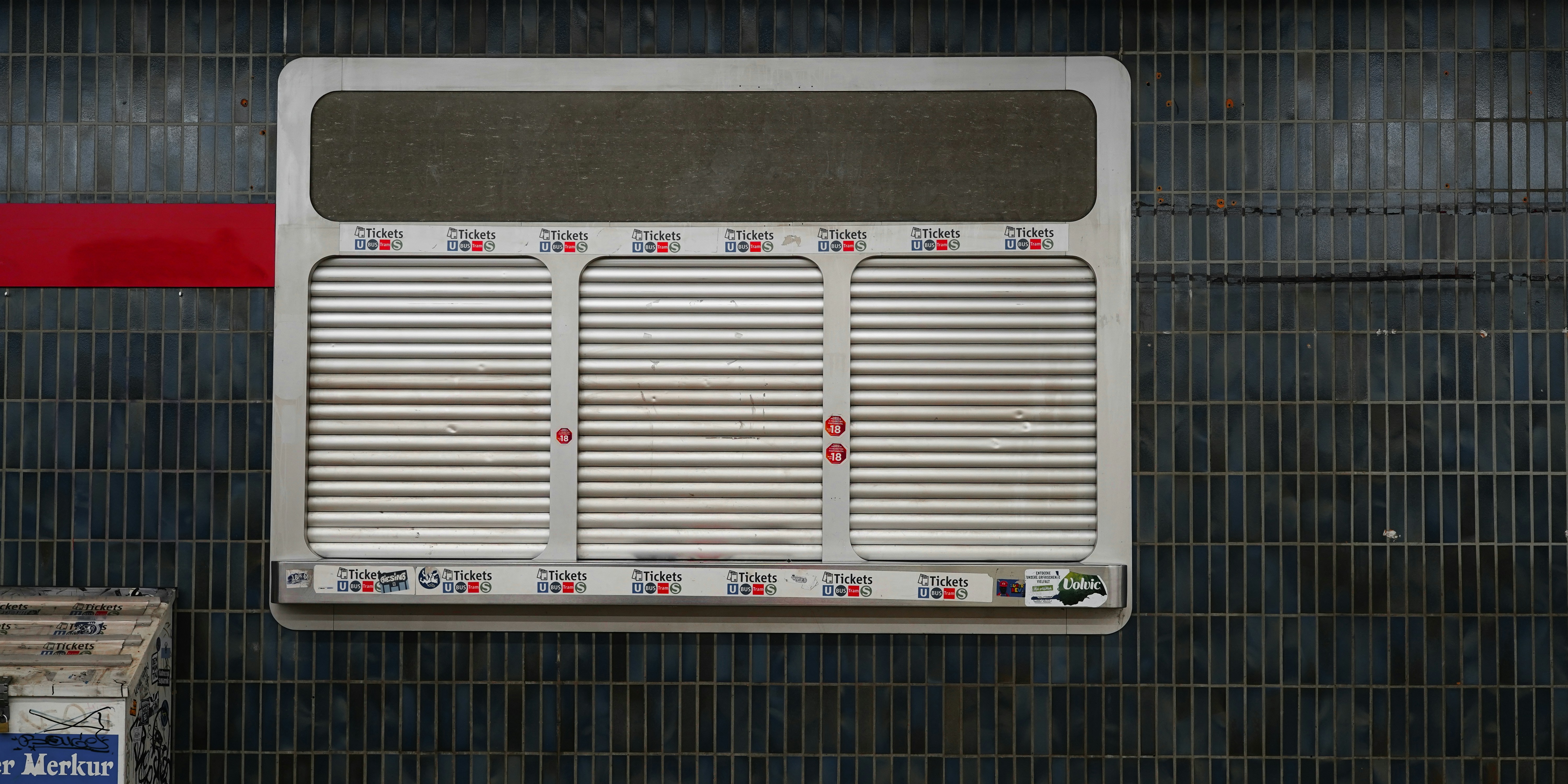 Metal vent with three horizontal slats centered on a dark tiled wall; a bold red stripe runs horizontally near the top, and a small blue-green label sits at the bottom edge. This is a photographic study of industrial texture.