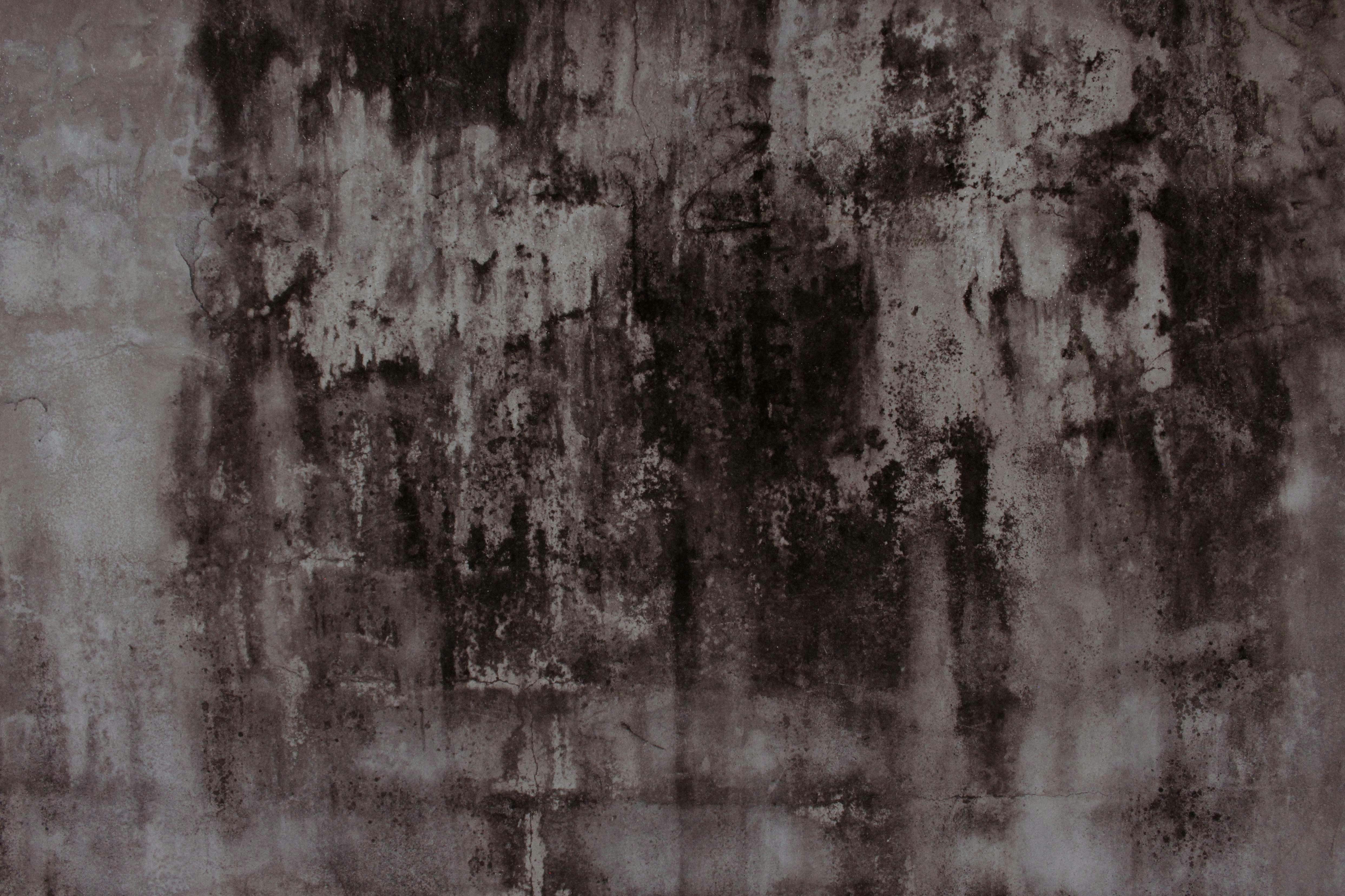 Granite-like wall texture with dark, irregular patches and a muted, iron-toned palette; a close-up of surface weathering without distinct subject or foreground elements.