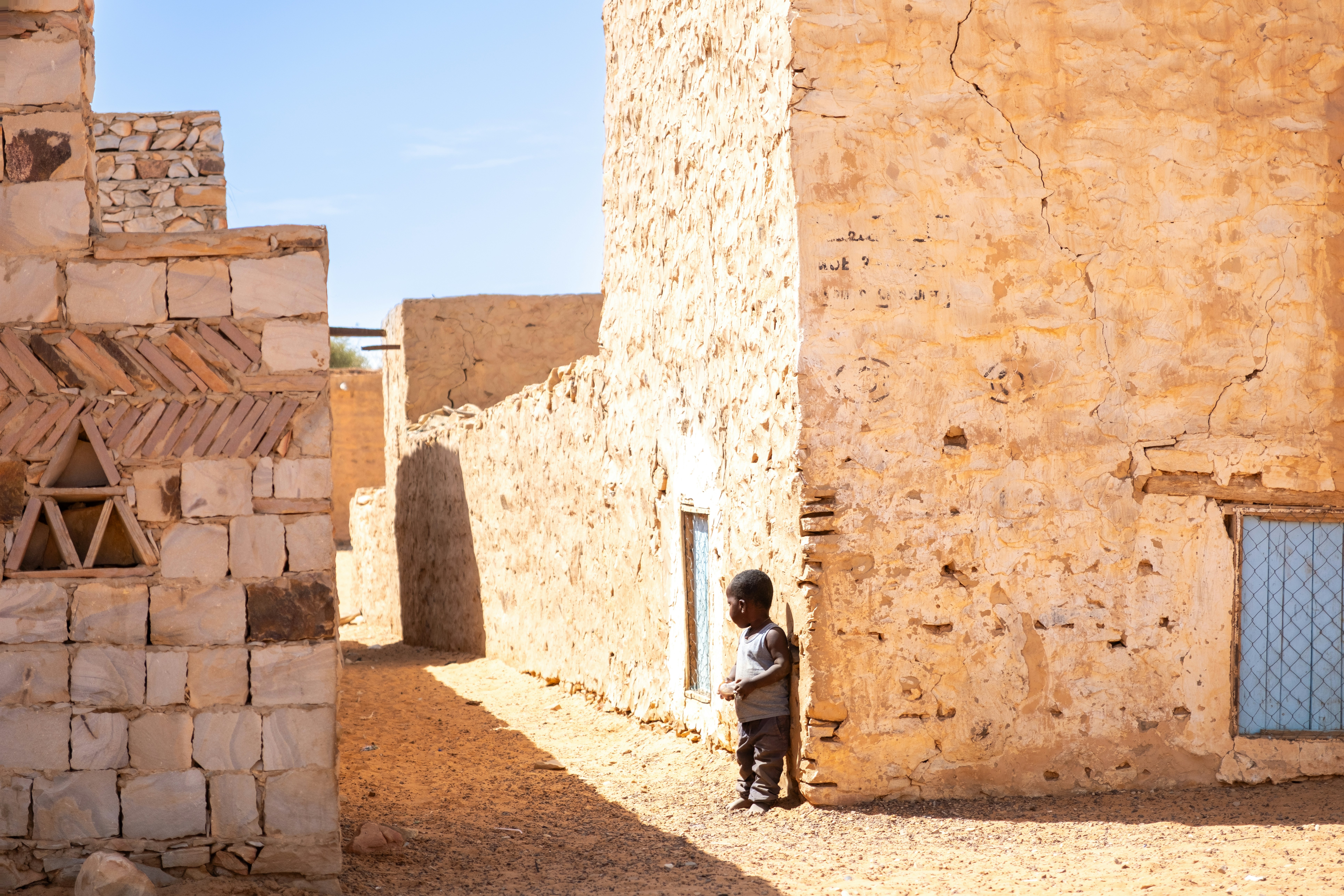 Child Peering from the Sunlit Alley of Earthen Walls