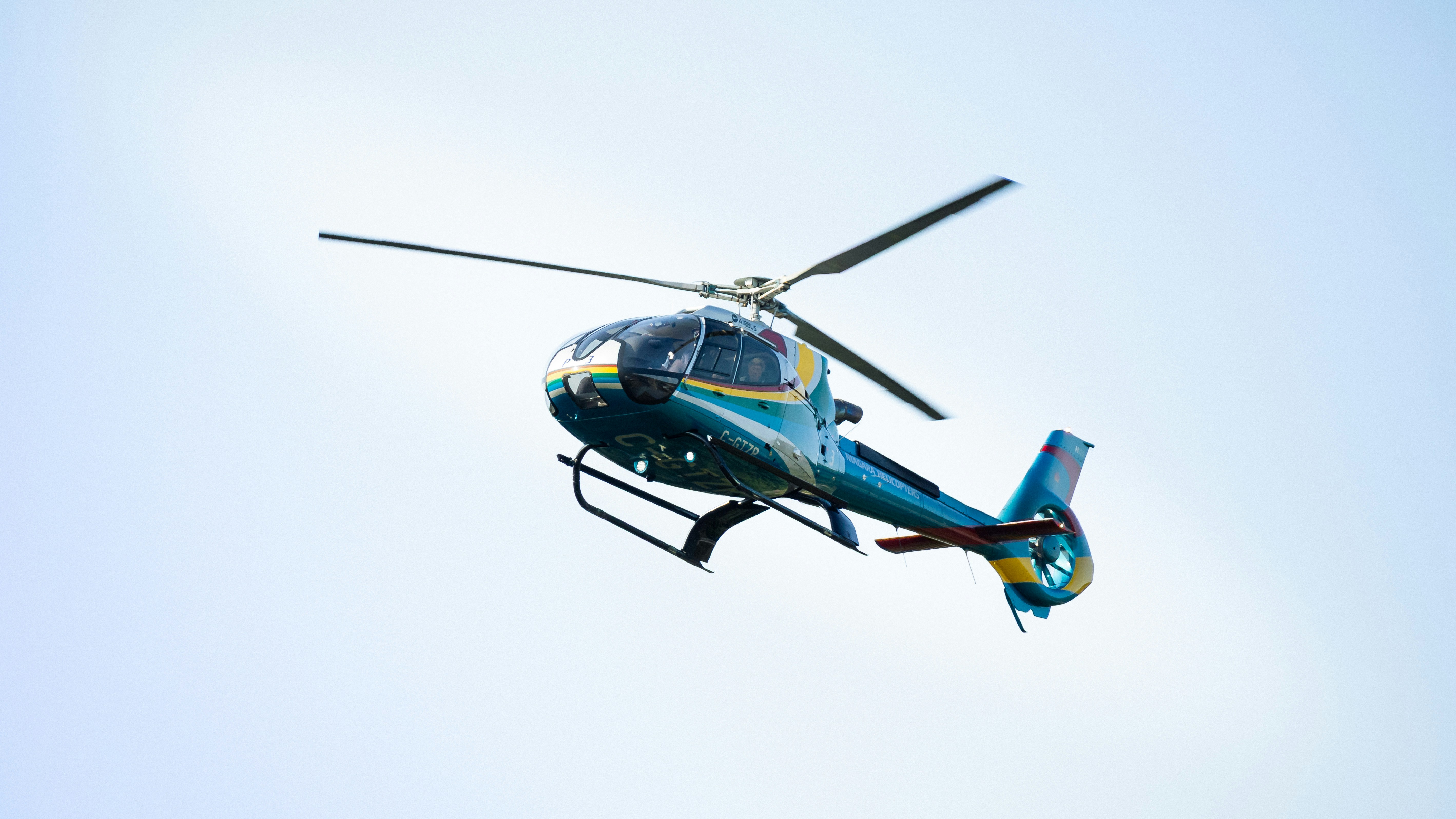 Blue rescue helicopter in mid-flight against pale sky, rotor blur hinting motion and emergency livery standing out.