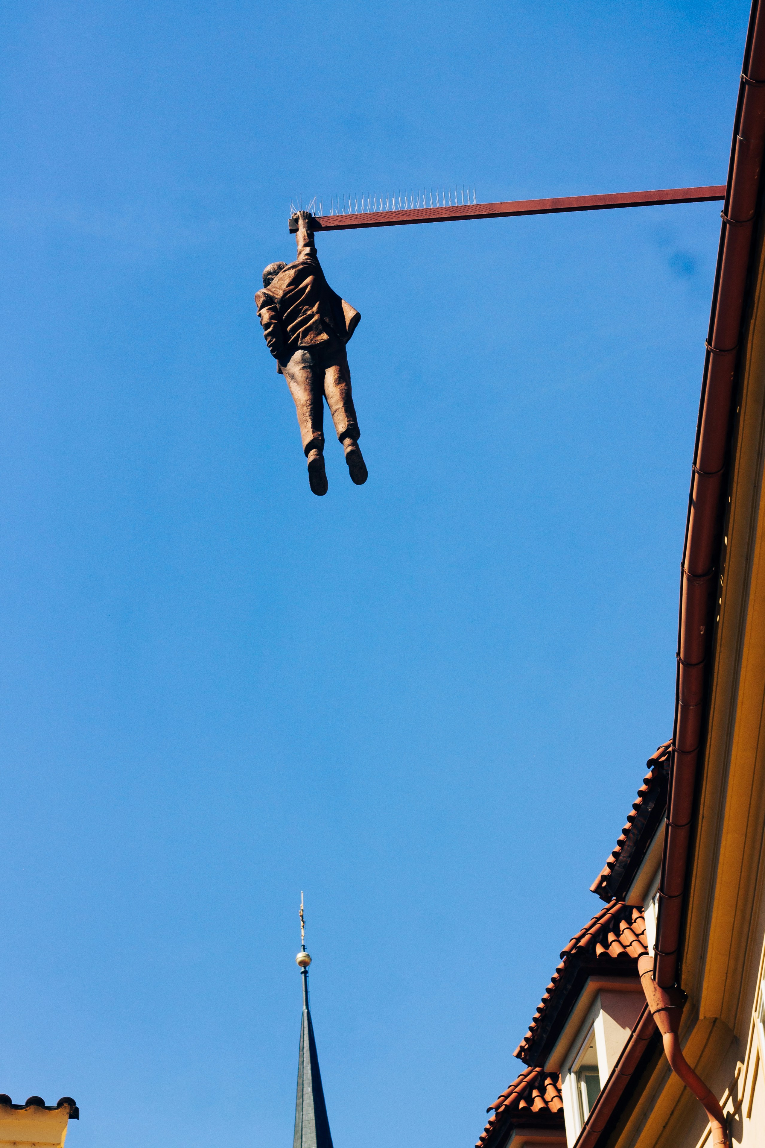 Daring Climb: Man Clings to a Narrow Metal Beam Against a Clear Sky