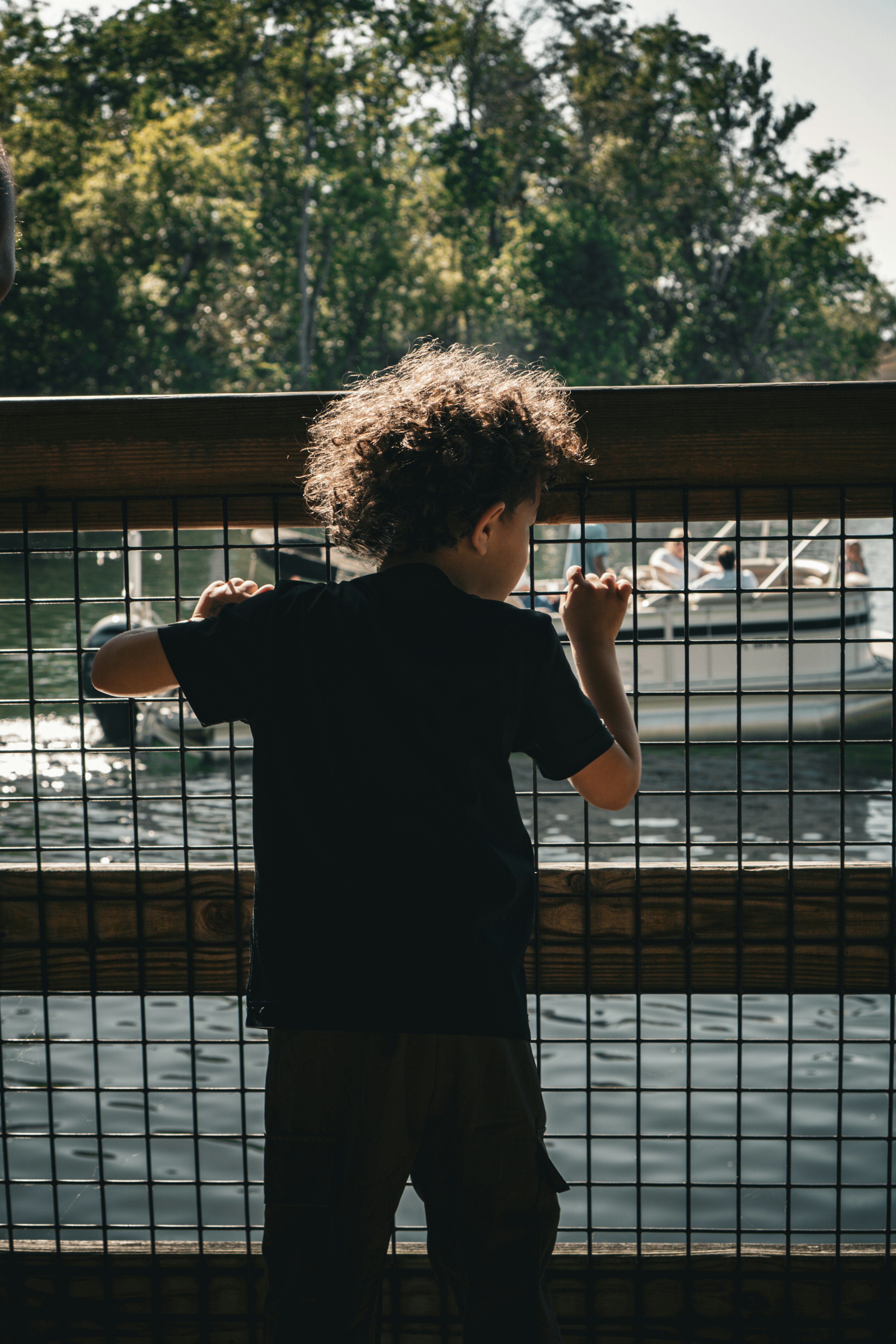 Child at the railing watching boats drift on sunlit water