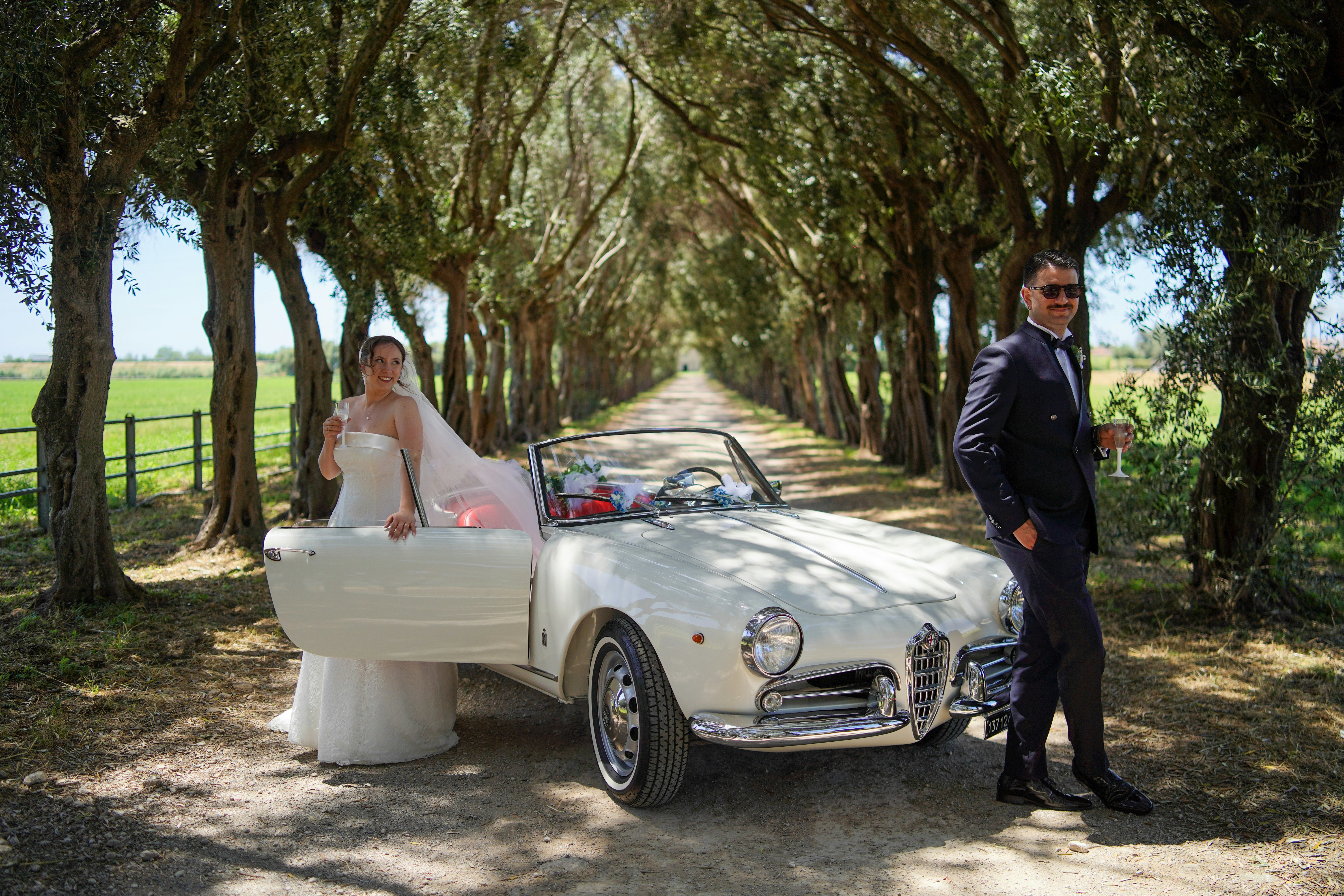 Bride and Groom Depart in a Vintage Convertible Under an Aisle of Trees
