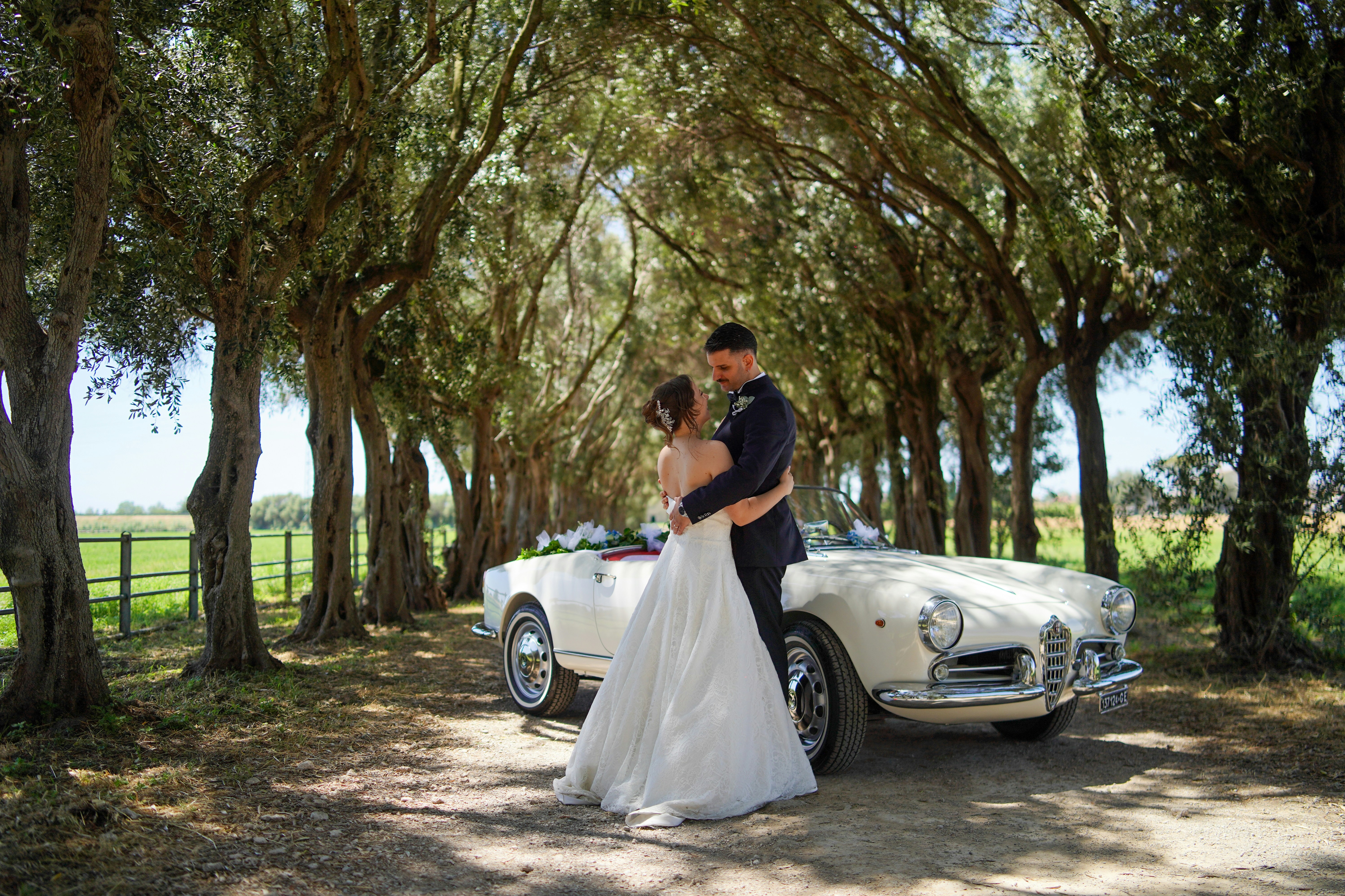 Elegance Under the Oaks: A Bride and Groom Share a Quiet Moment by a Classic Convertible