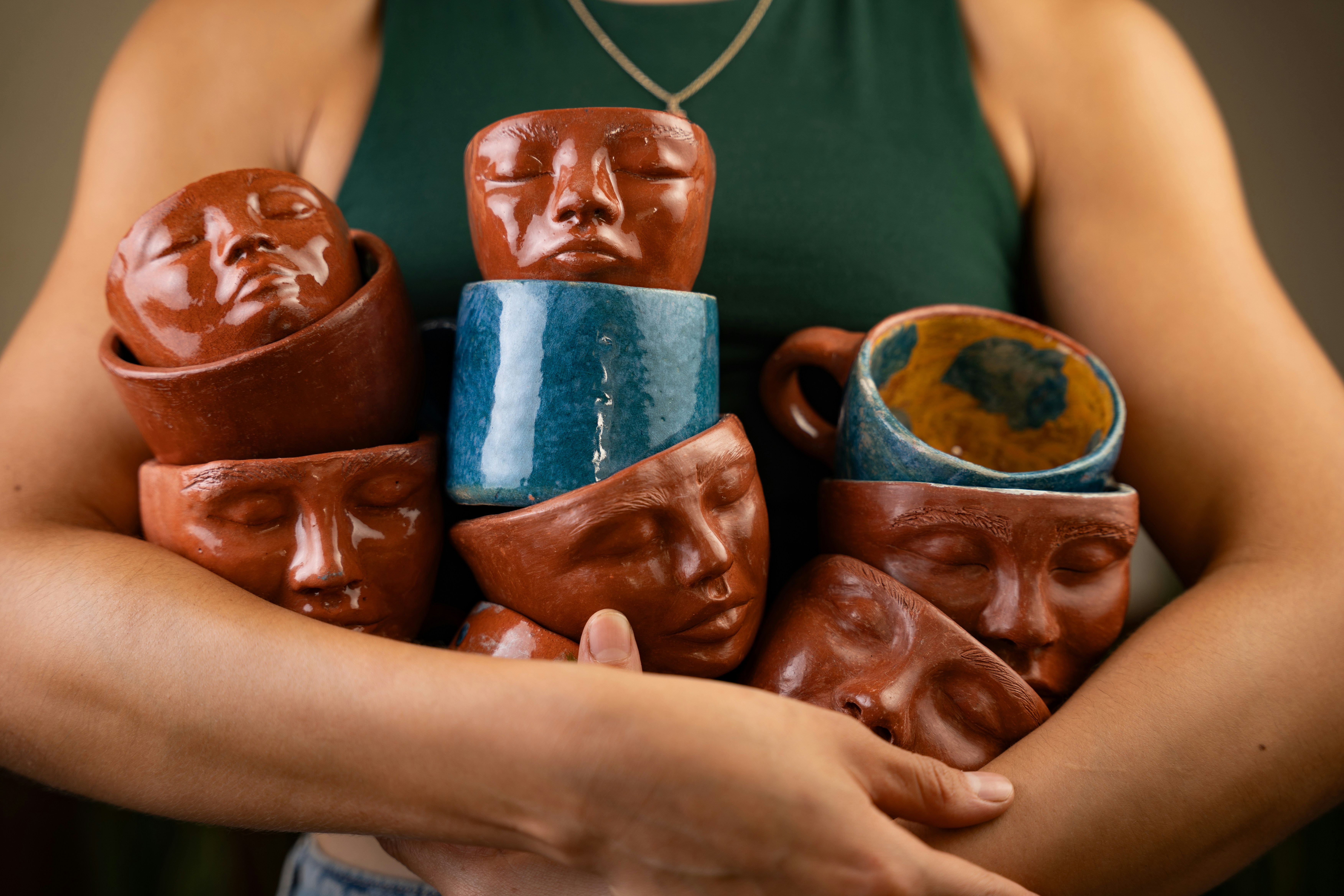 Hands full of clay-ware faces: a soft embrace of ceramic mugs