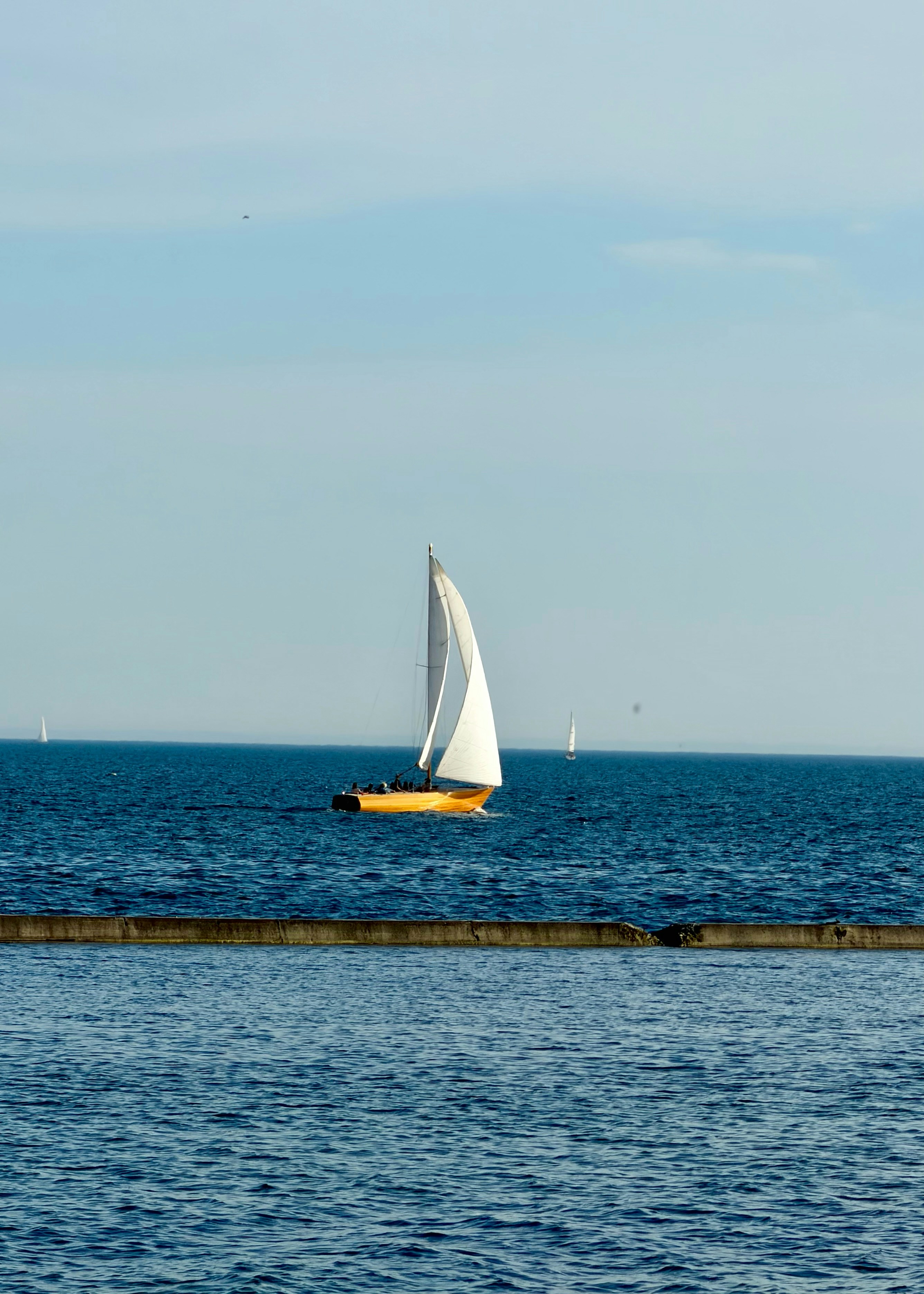 Yellow sailboat at the horizon, cutting through calm sea