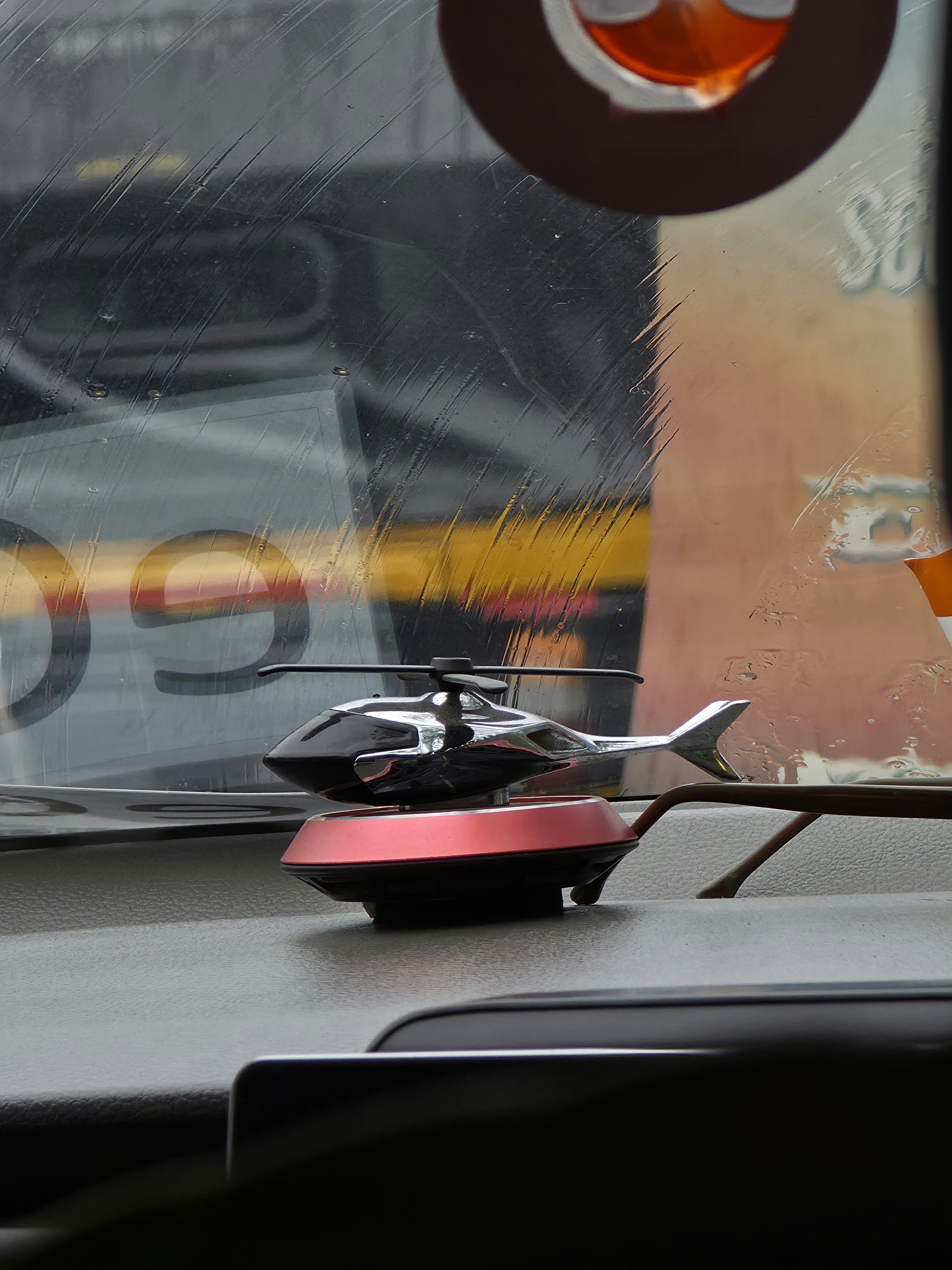 Sleek toy helicopter glides across a glossy car dash, captured through a rain-slick windshield