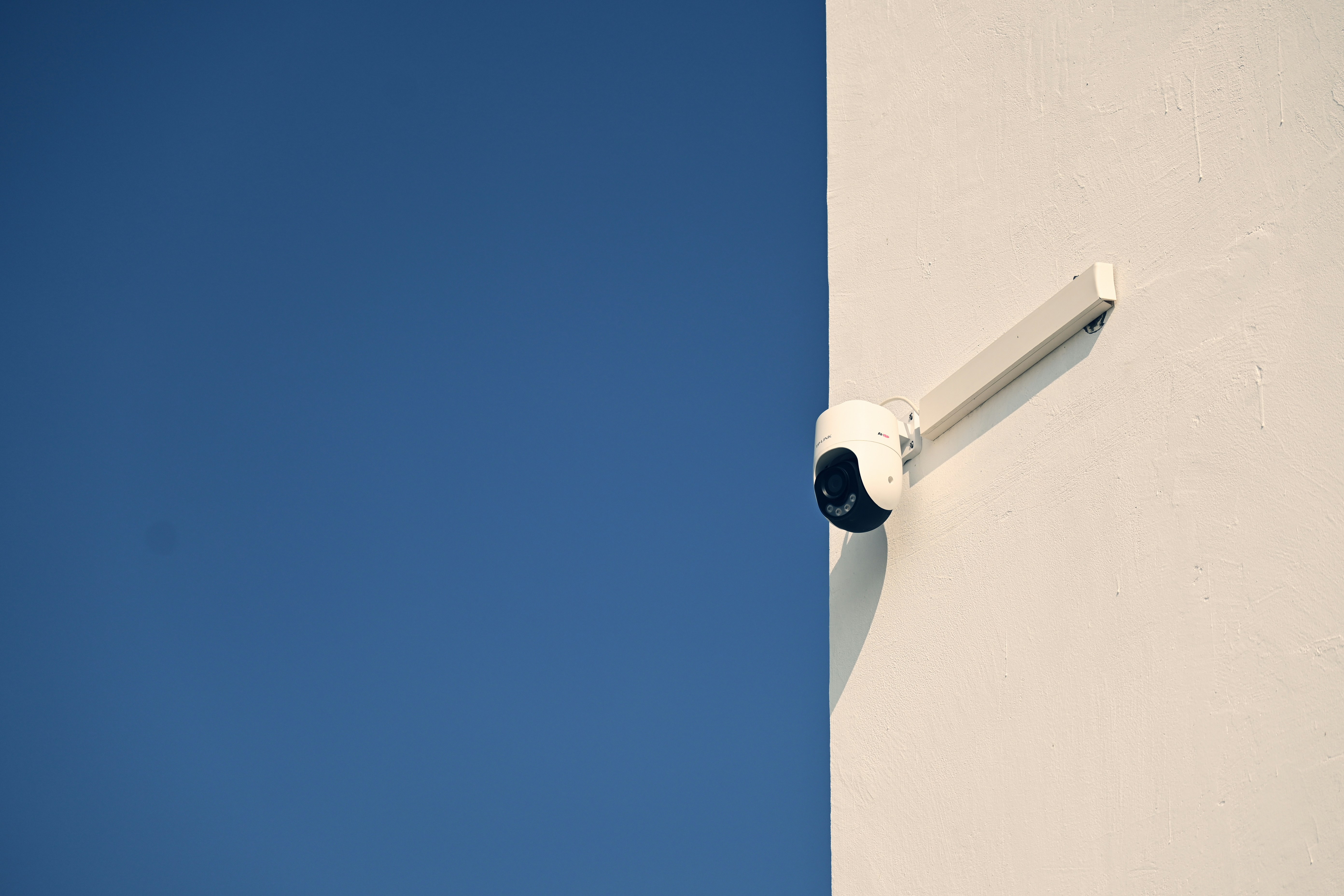 Minimalist Corner: A Security Camera Clings to White Facade under Deep Blue Sky