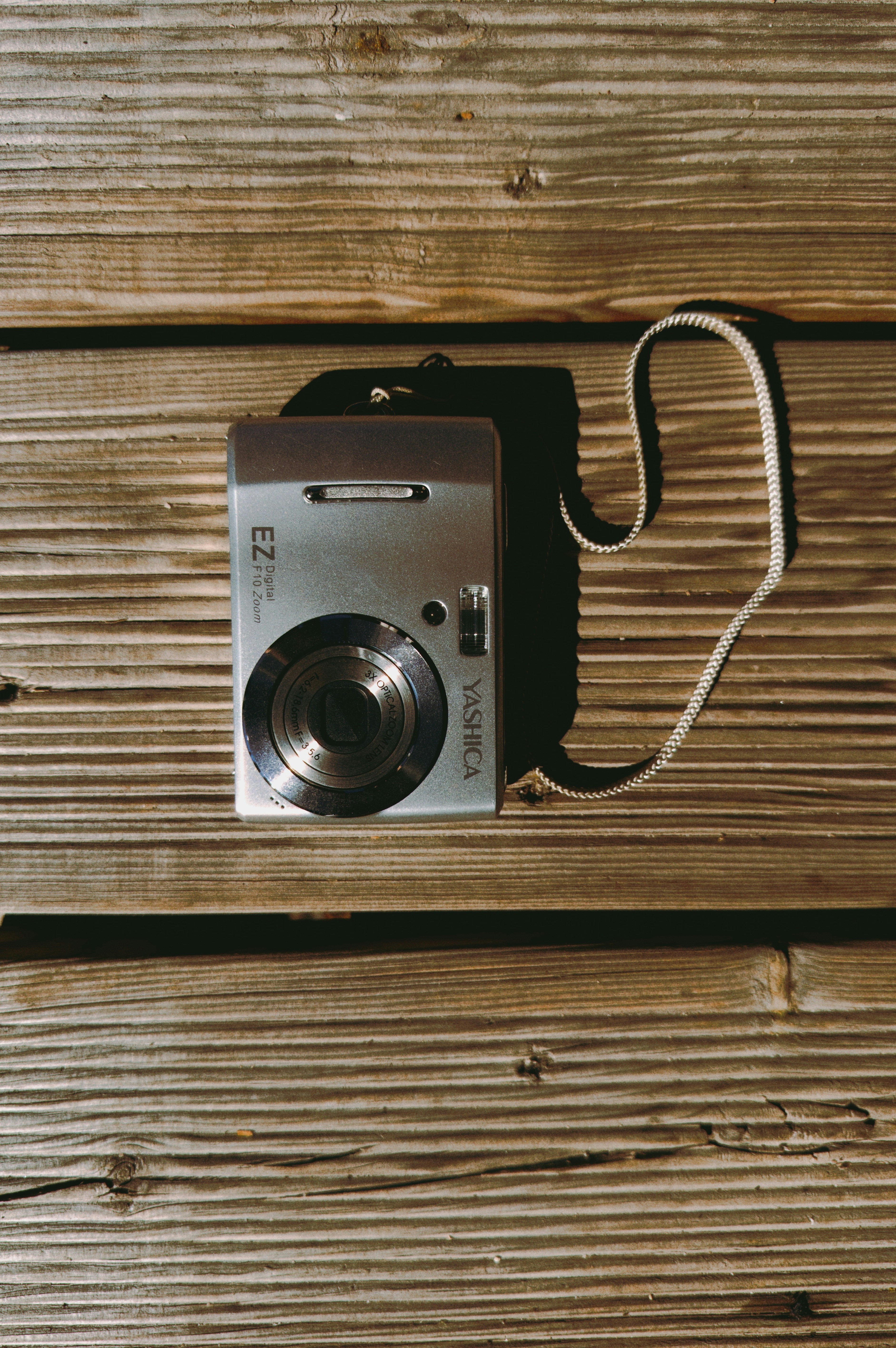 A silver digital camera with a strap on wooden planks.