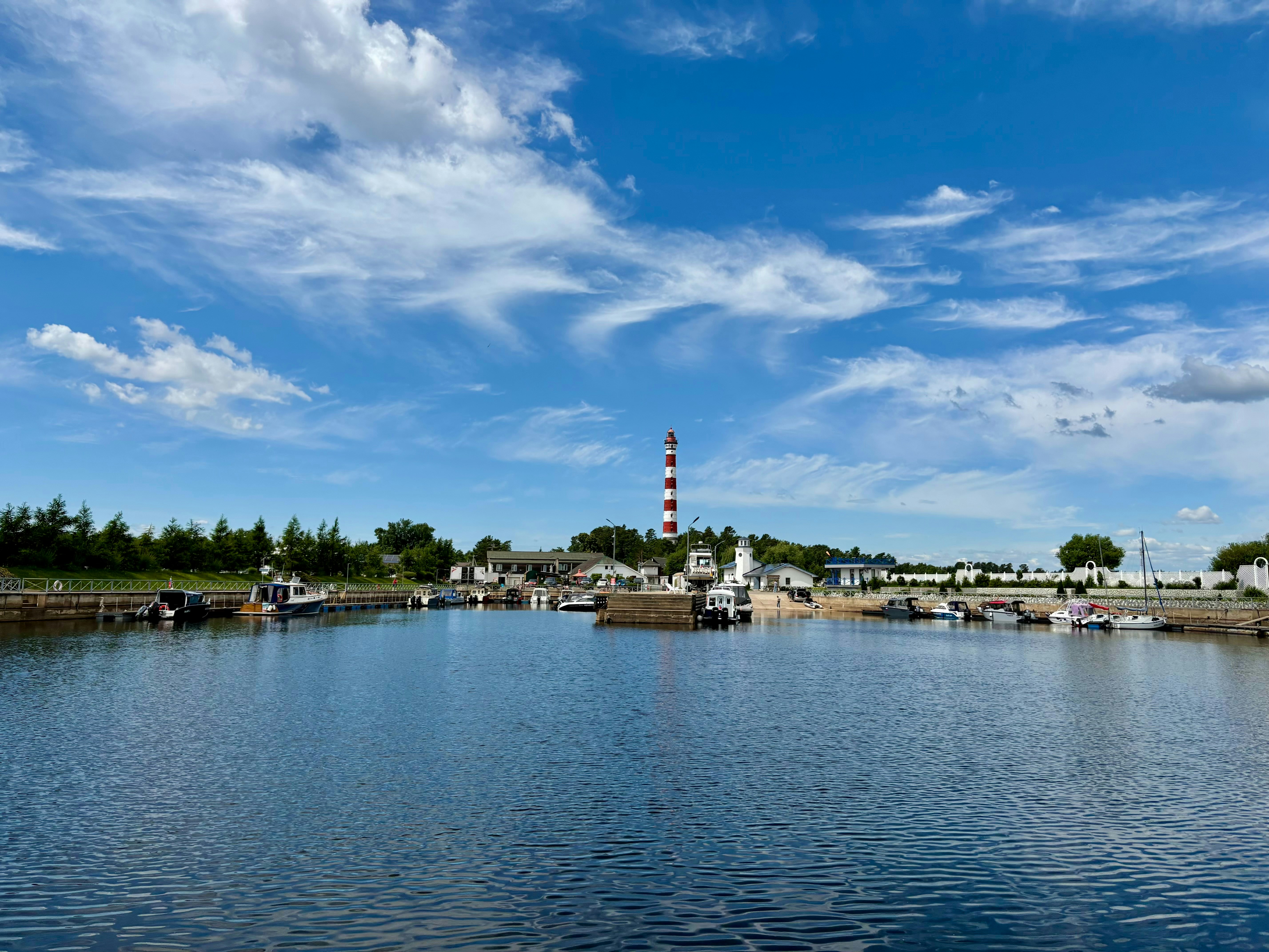 Harbor Mirror: Boats, Dock, and a Striped Lighthouse Under Wide Sky