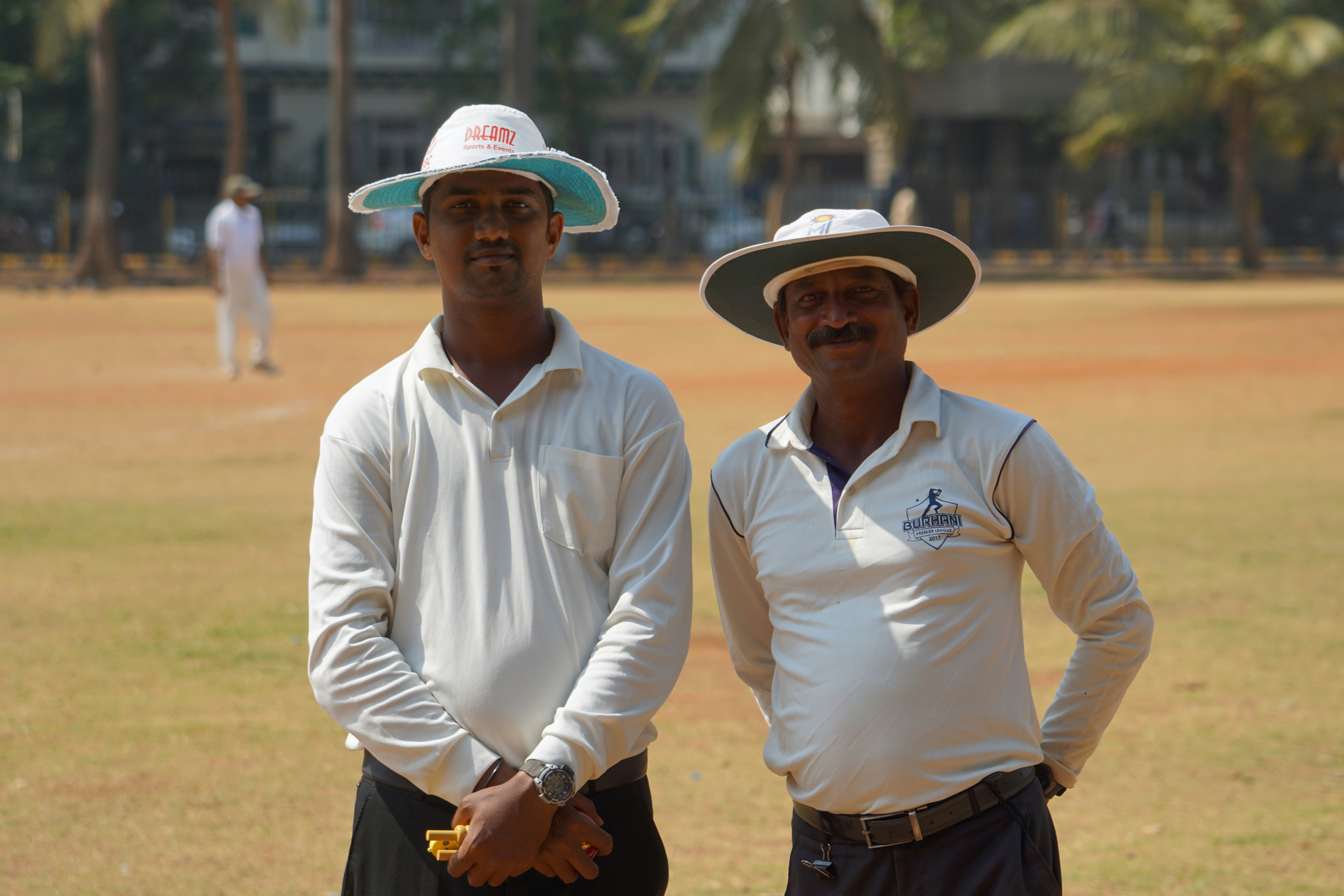Two Cricket Coaches Stand in Sunlit Field, Hoodie and Hats Cast in Warm Light