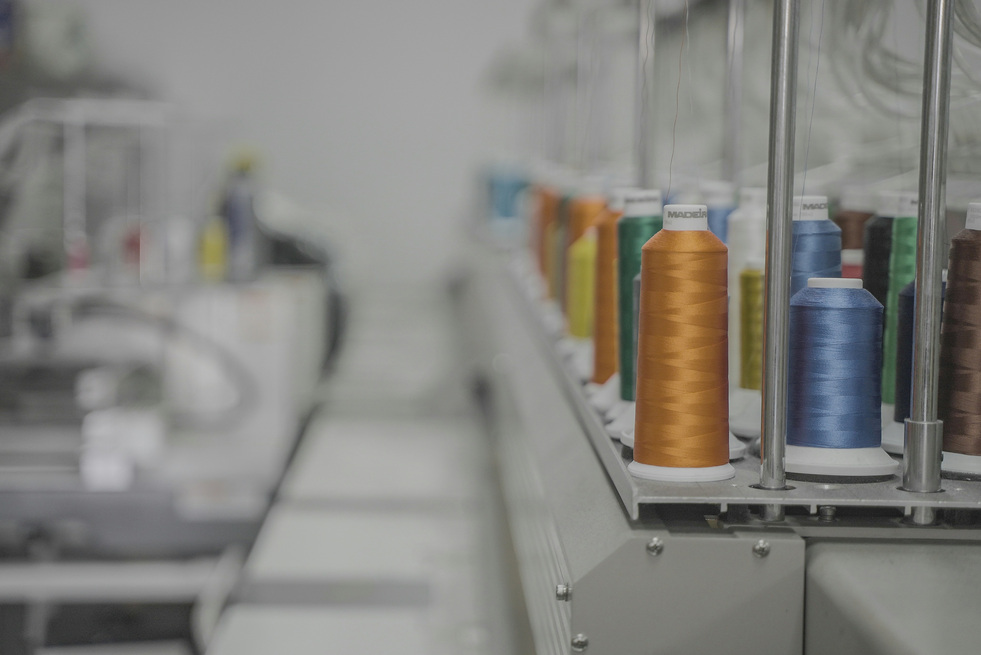 Rows of colored thread spools line a textile machine, with a shallow depth of field drawing attention to the vibrant centerpiece while the background fades away.