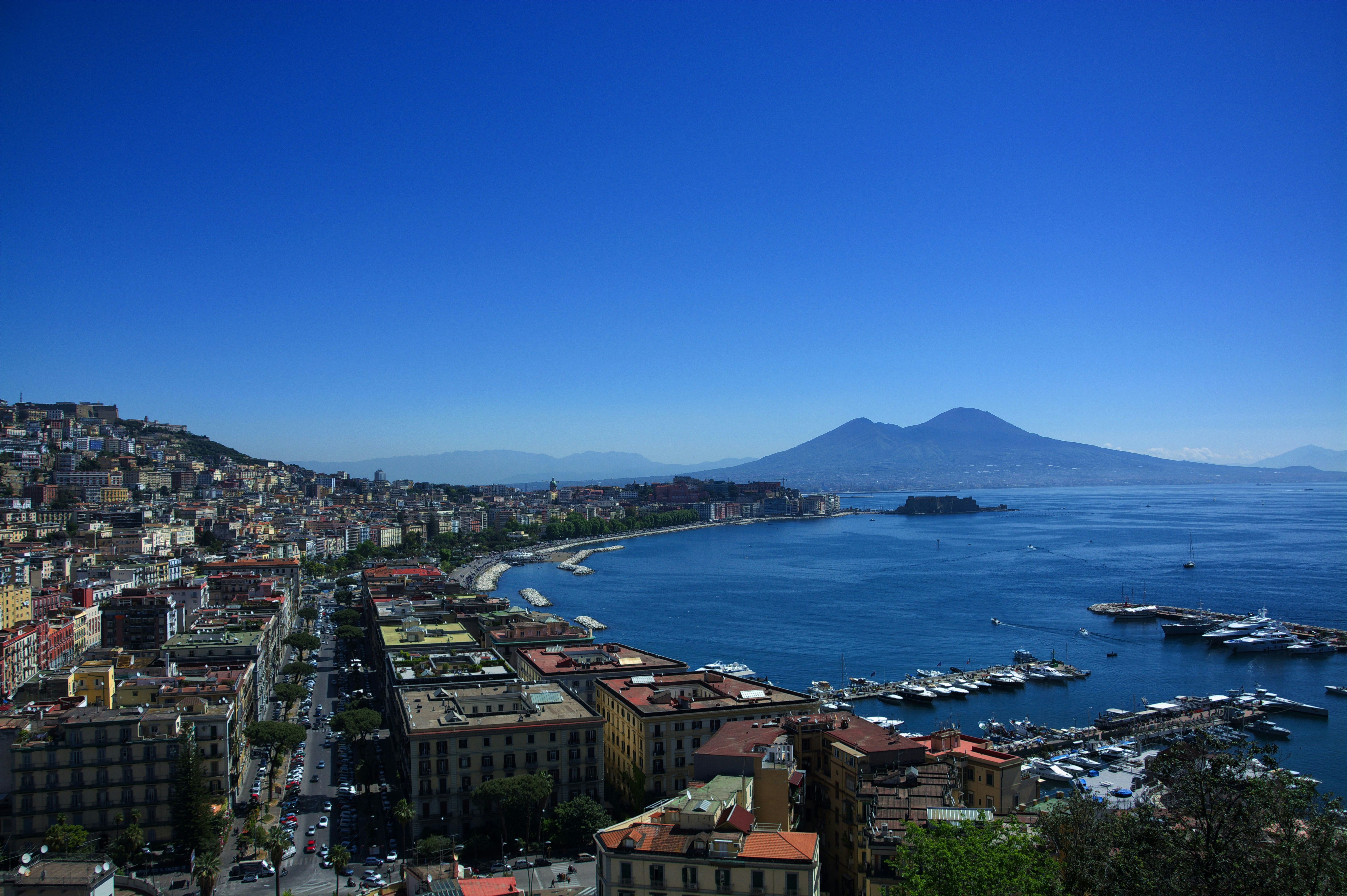 Port town and marina bask in Mediterranean light with a distant volcanic backdrop