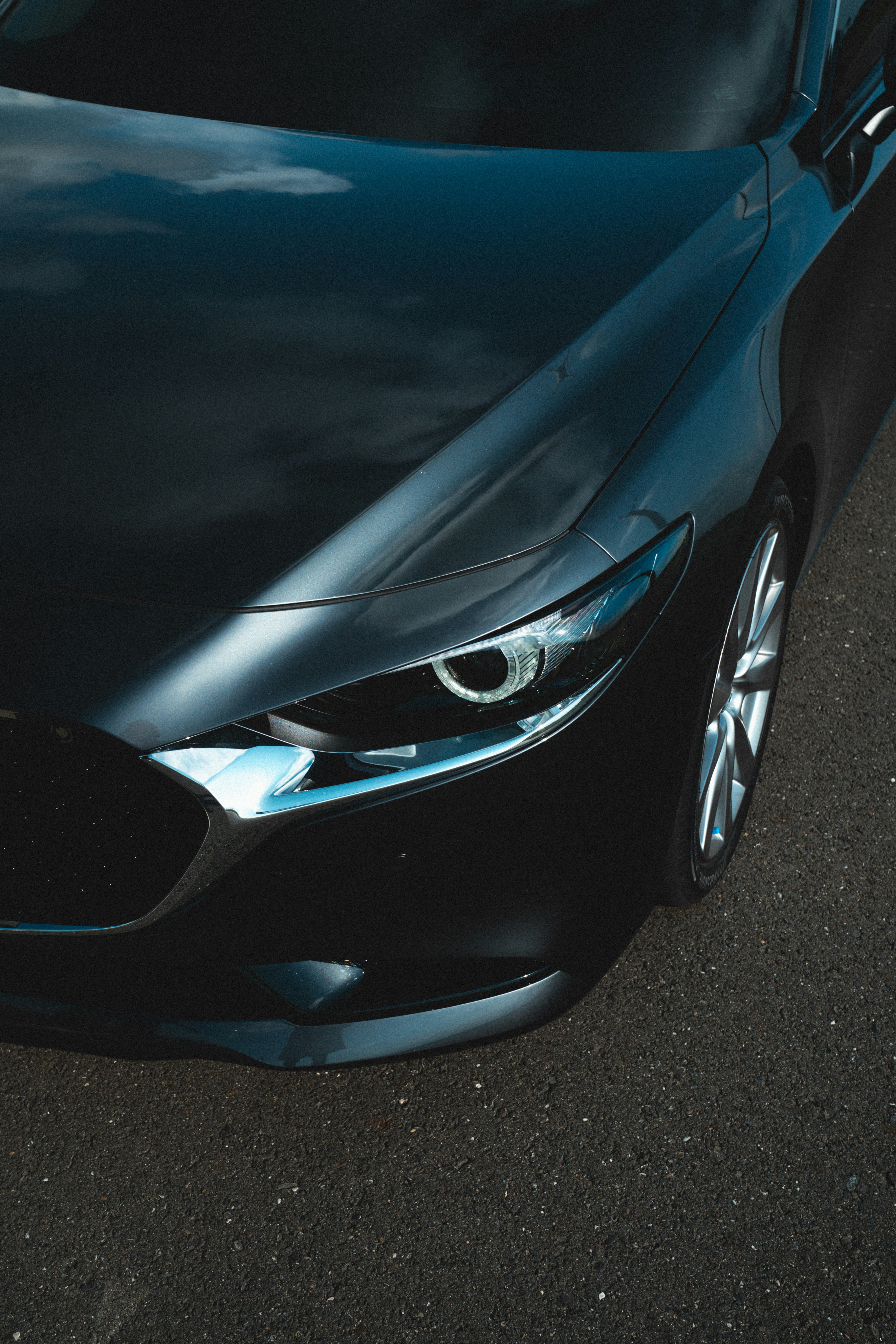 Close-up view of a metallic blue car with a sharp headlight and angular hood, emphasizing metallic reflections and contours. This is a high-contrast automotive shot.