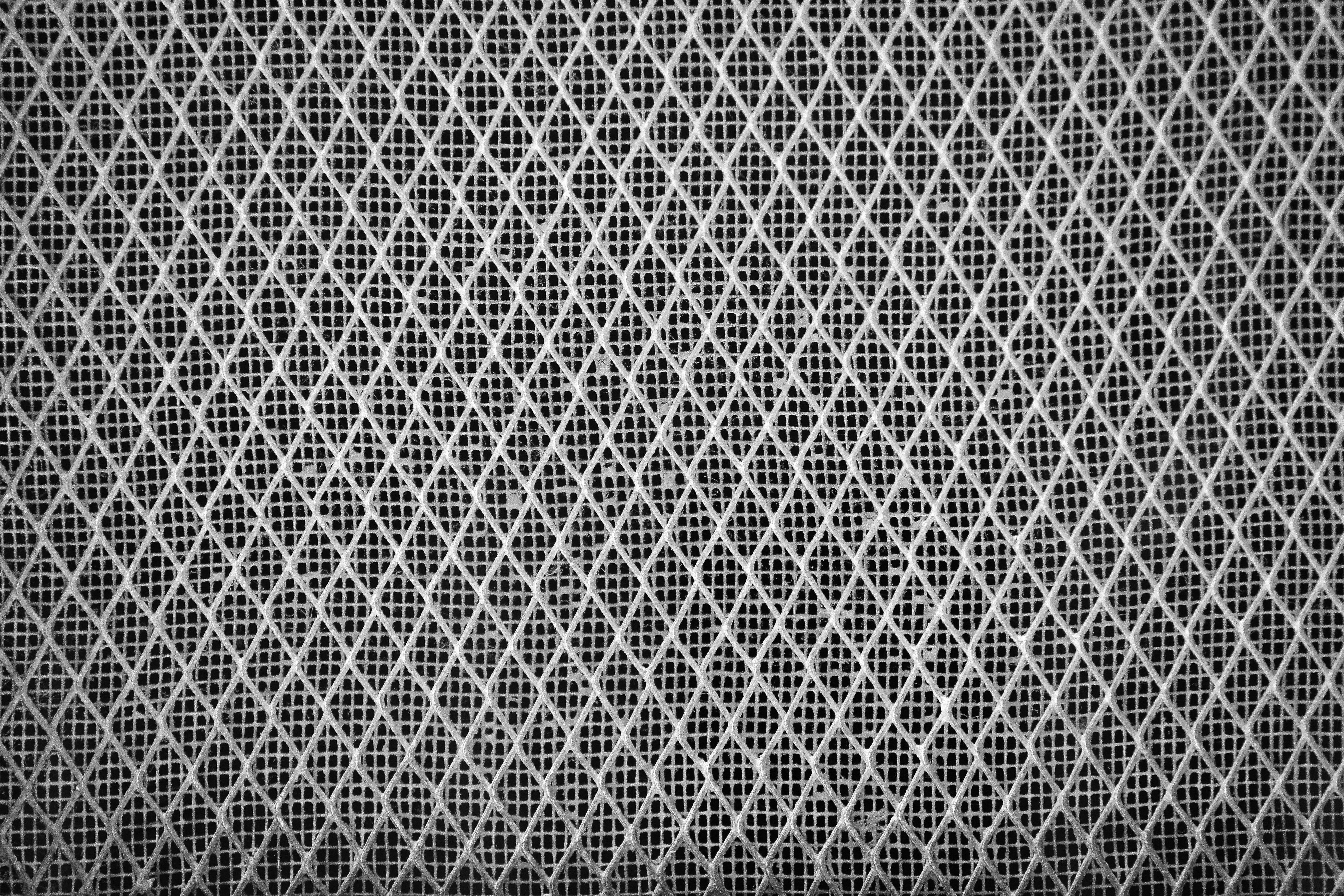 Close-up of a diamond-pattern metal mesh surface, emphasizing texture and repetition for industrial design analysis. This is a detailed macro-style capture of a metal grate surface.