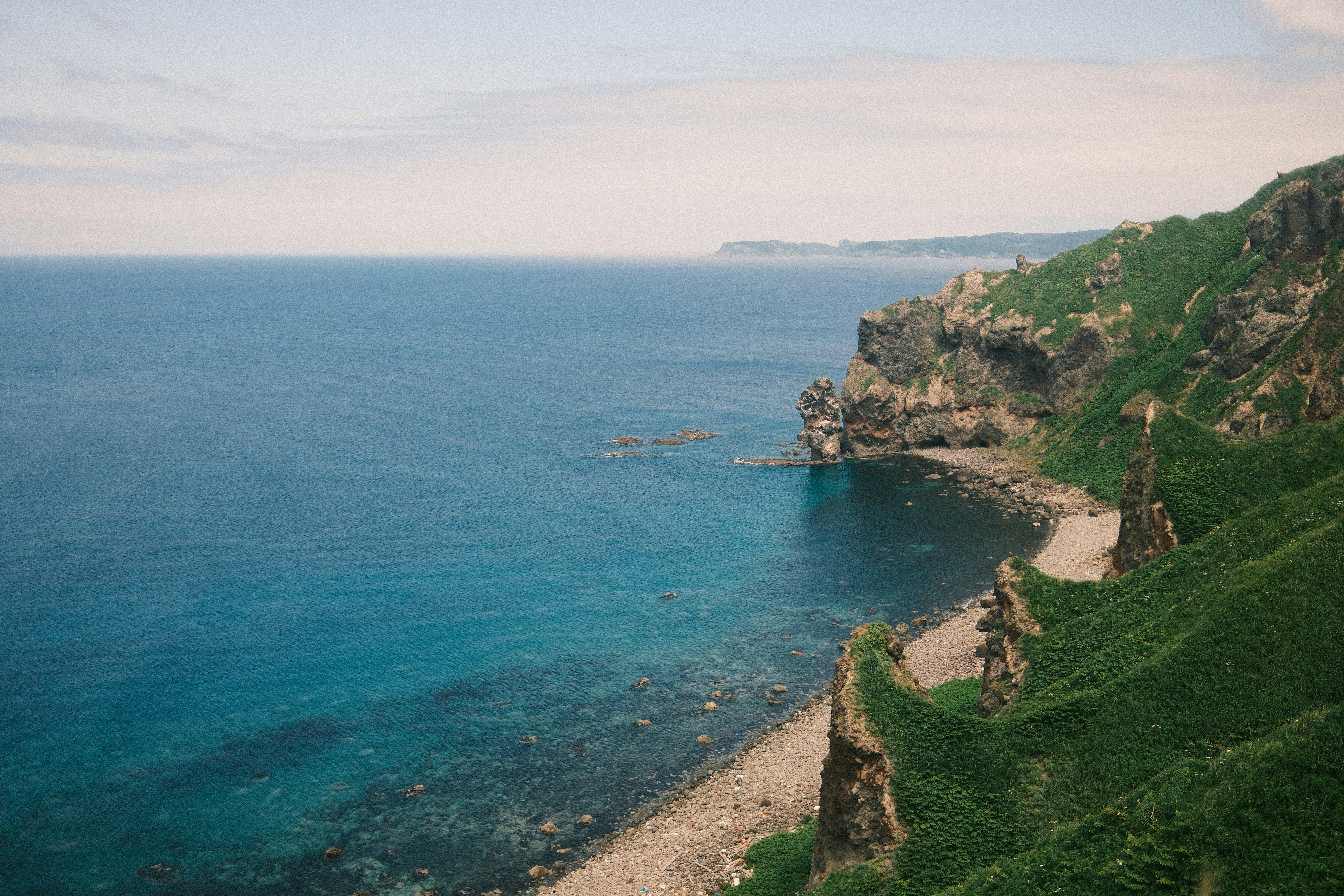 Vast blue ocean meets rugged green cliffs and rocky shore.