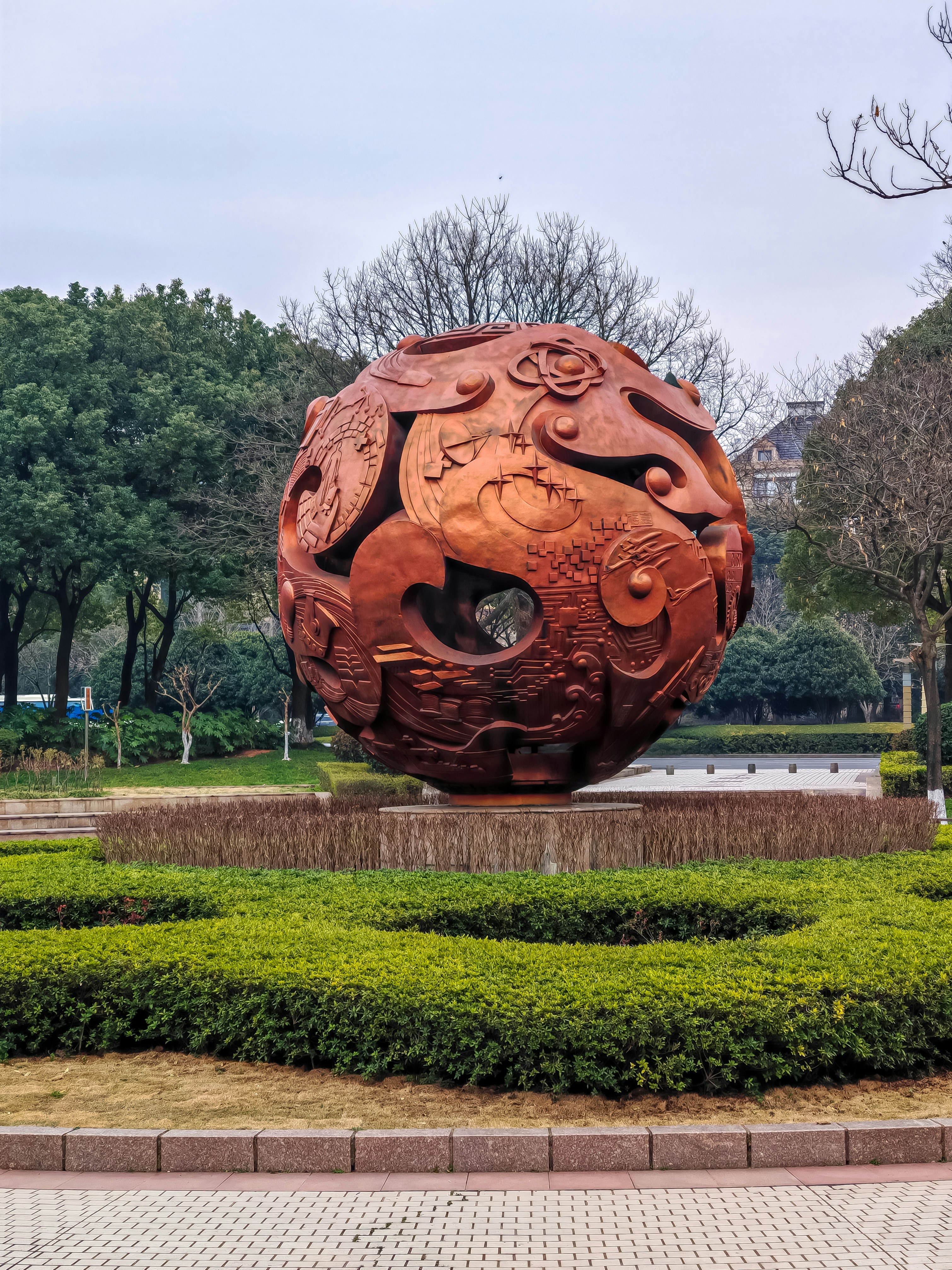 Terracotta sculpture centerpiece framed within a landscaped park, with trimmed hedges and trees in the background.