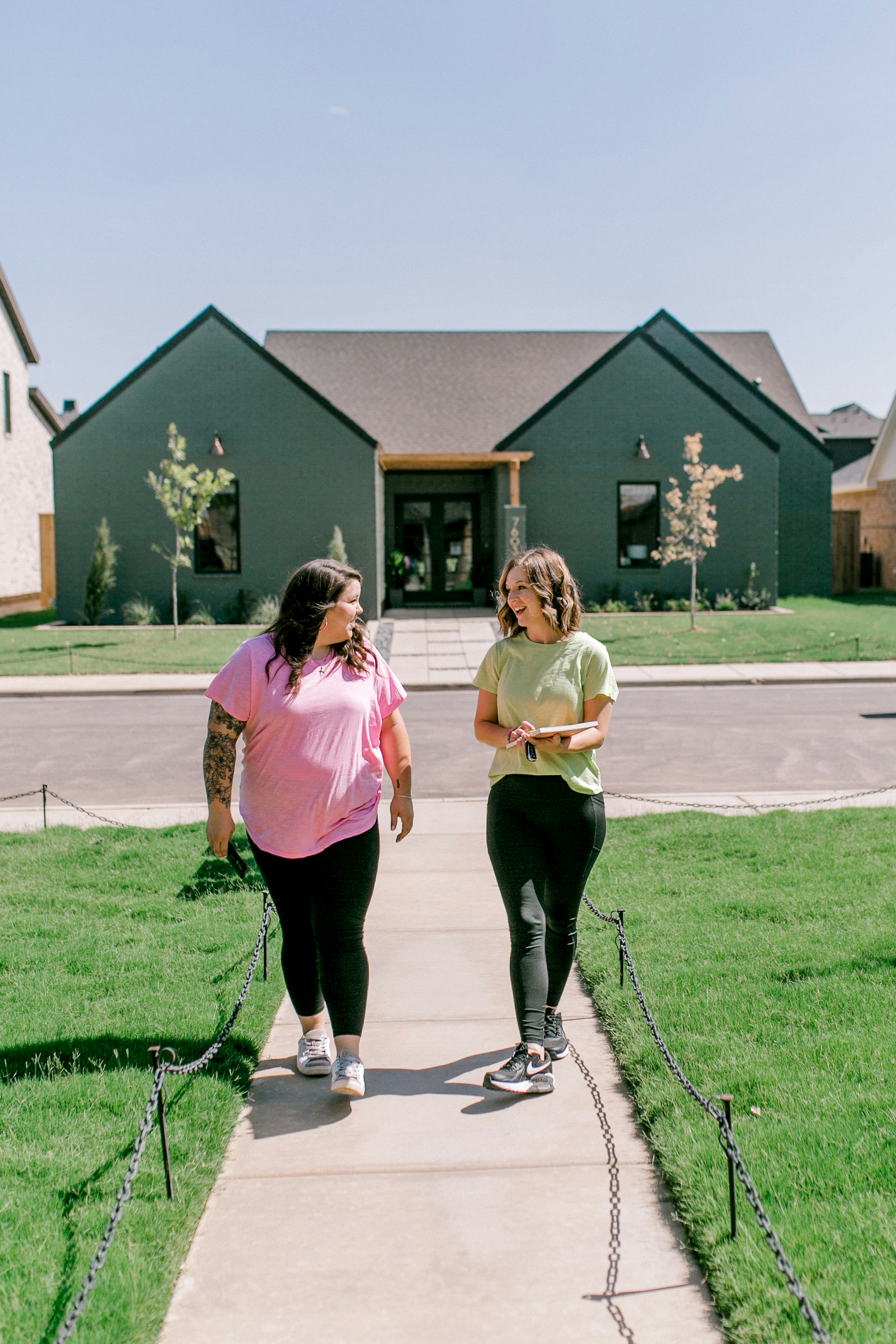 Two women converse while walking past a modern house.
