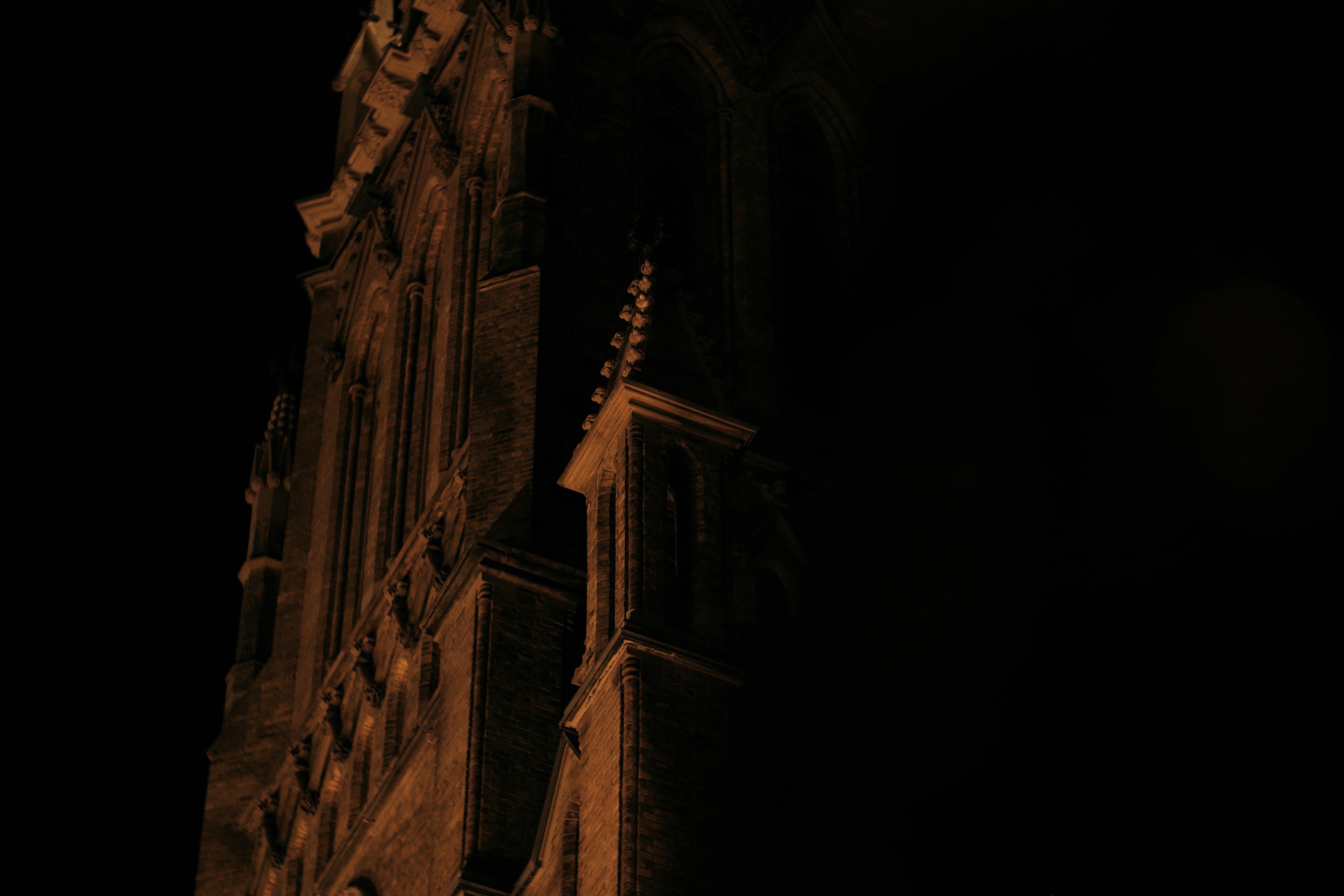 Dark, moonlit church spire rises with detailed masonry; minimal ambient light reveals texture and vertical lines against black sky.