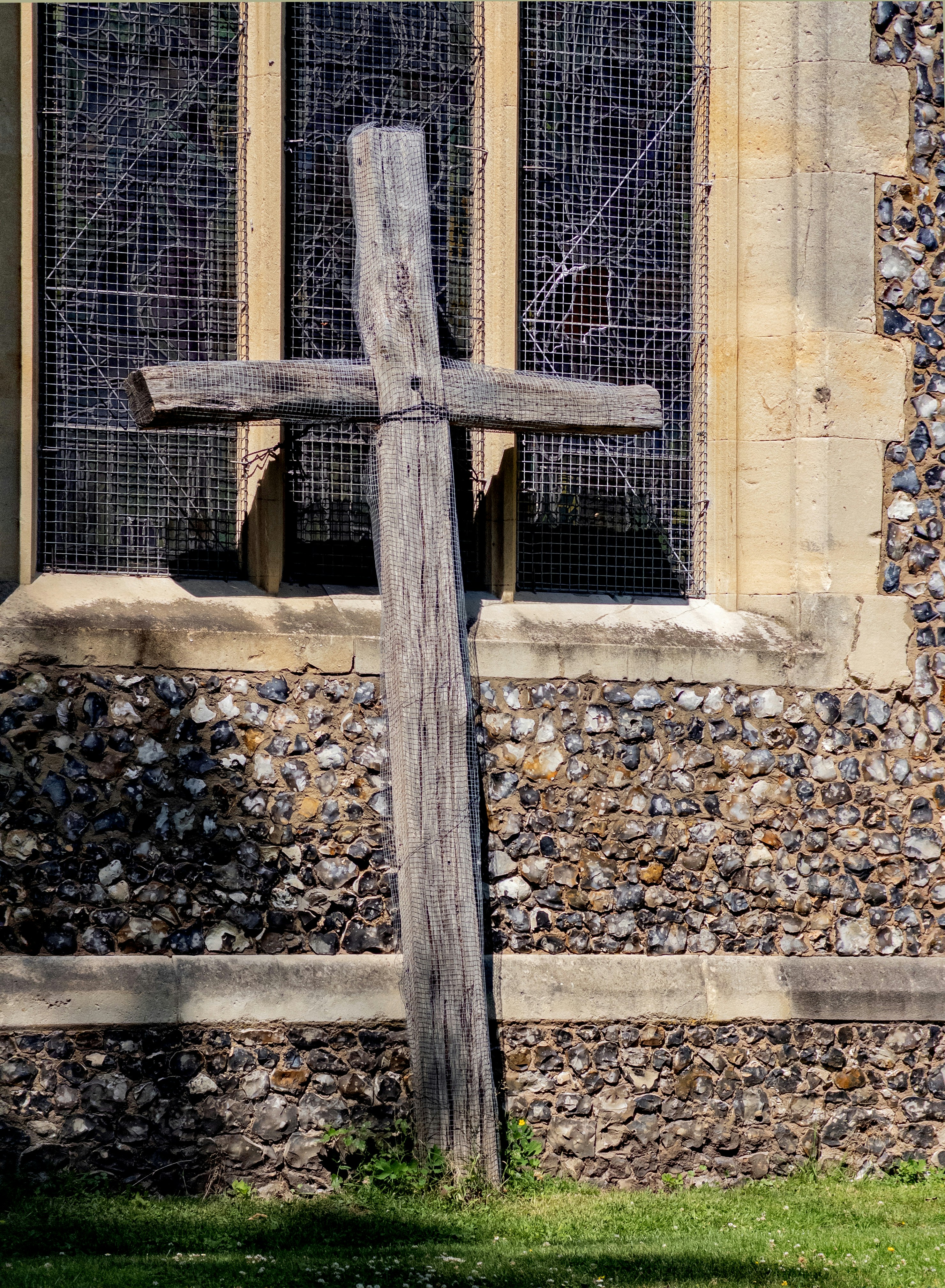 Weathered cross stands anchored against church wall