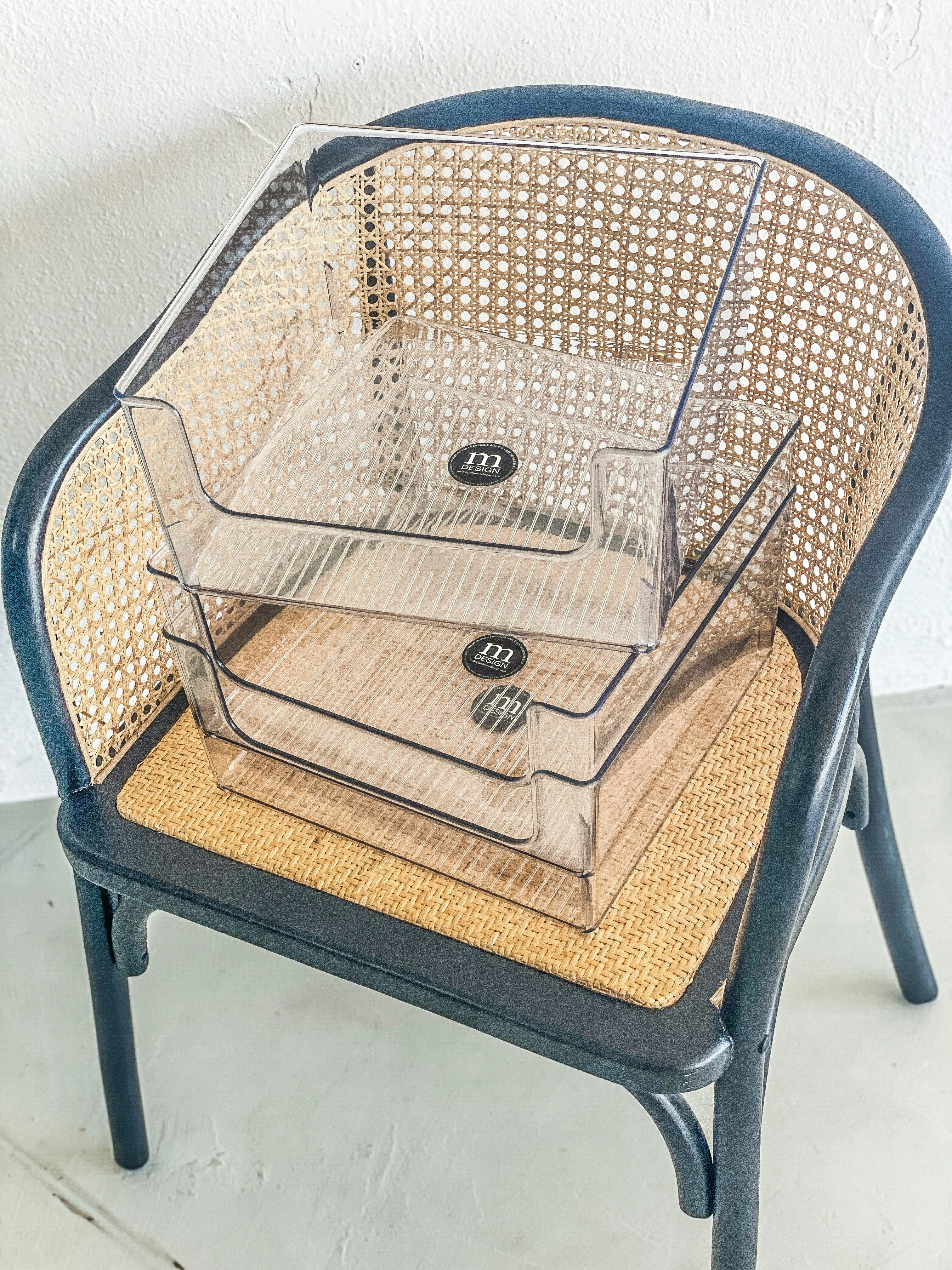 Clear nested boxes sit on a woven seat of a blue chair against a pale wall, creating a minimalist still life.
