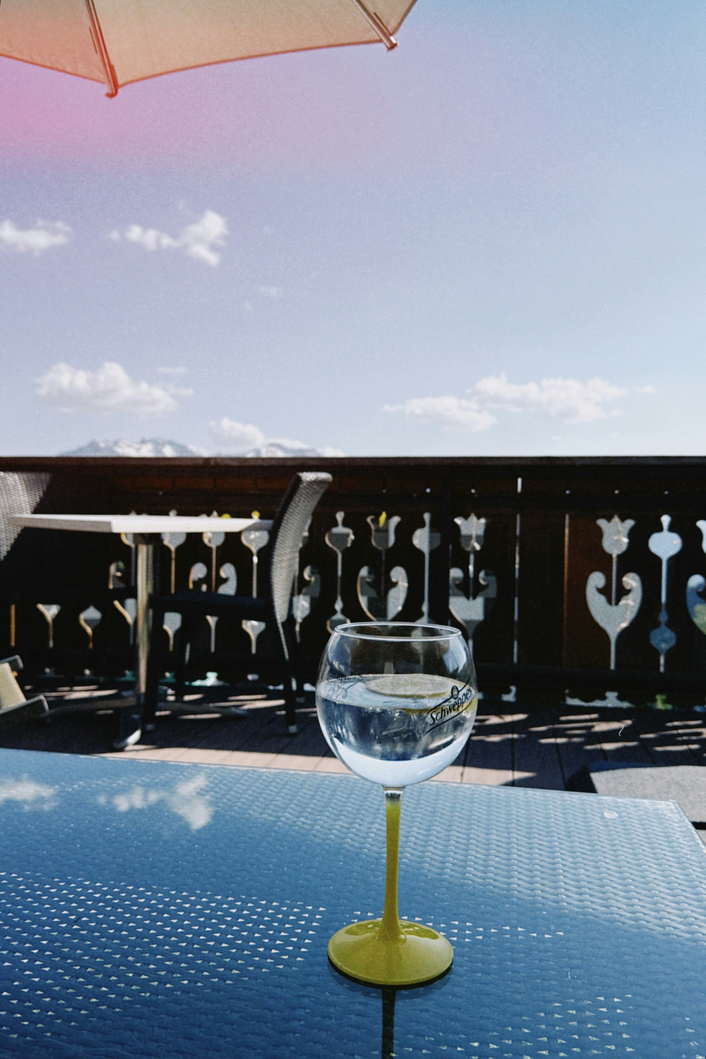Sunlit Terrace: Glass of Water on a Blue Table beneath a Coral Umbrella