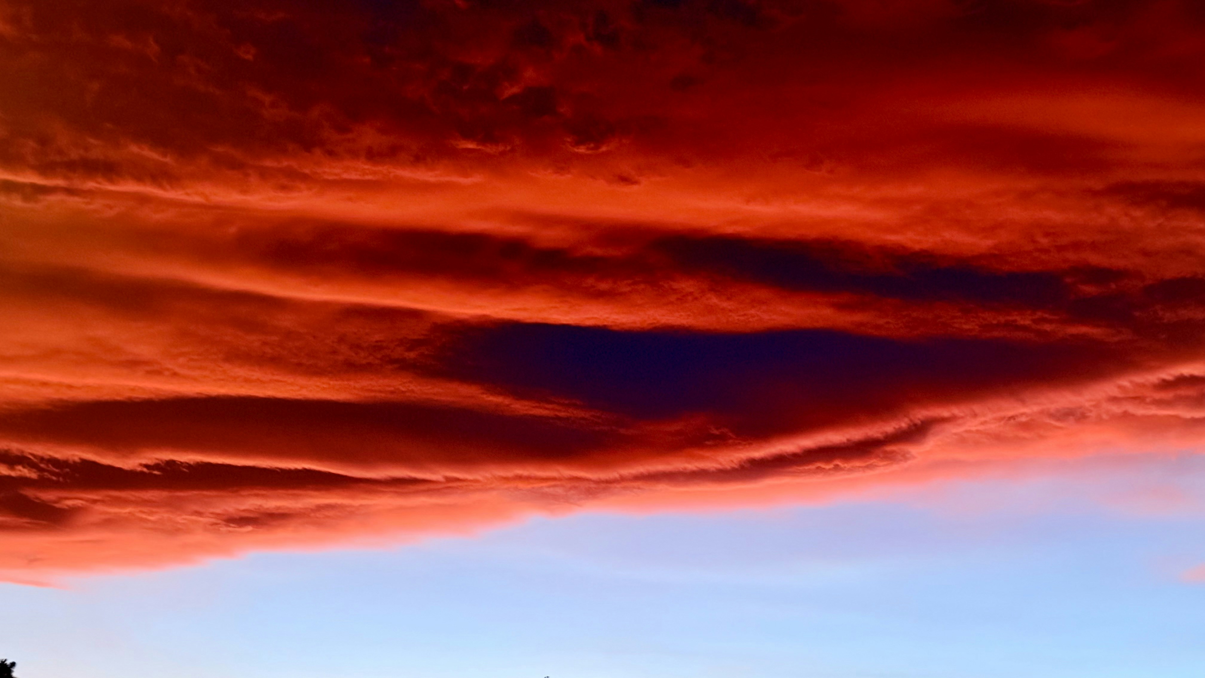A dramatic sunset gradient with deep red clouds resting above a pale horizon, casting a calm, expansive mood across the landscape.