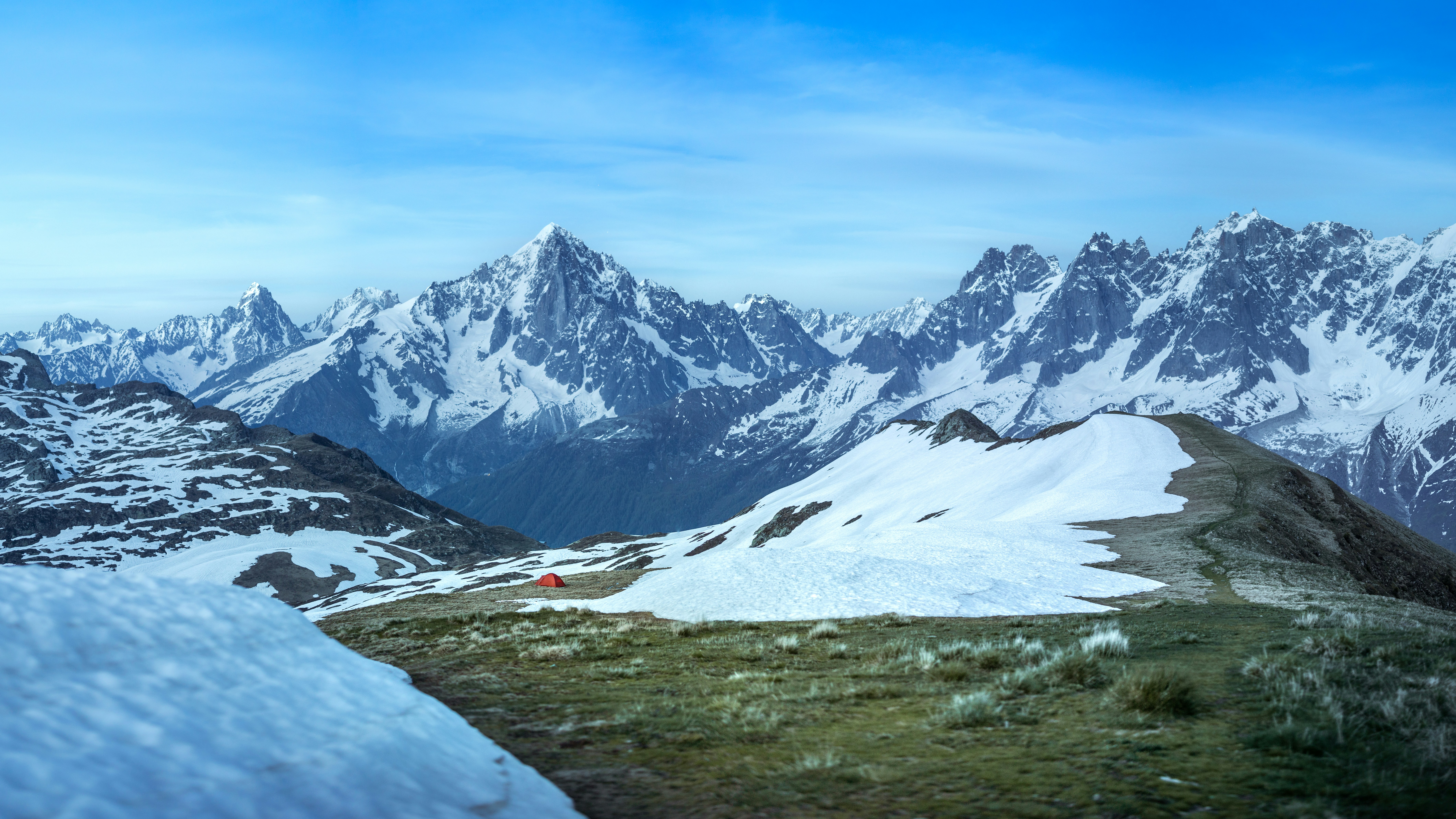 Snow-Capped Vistas: A Lone Red Tent Amid Alpine Grass