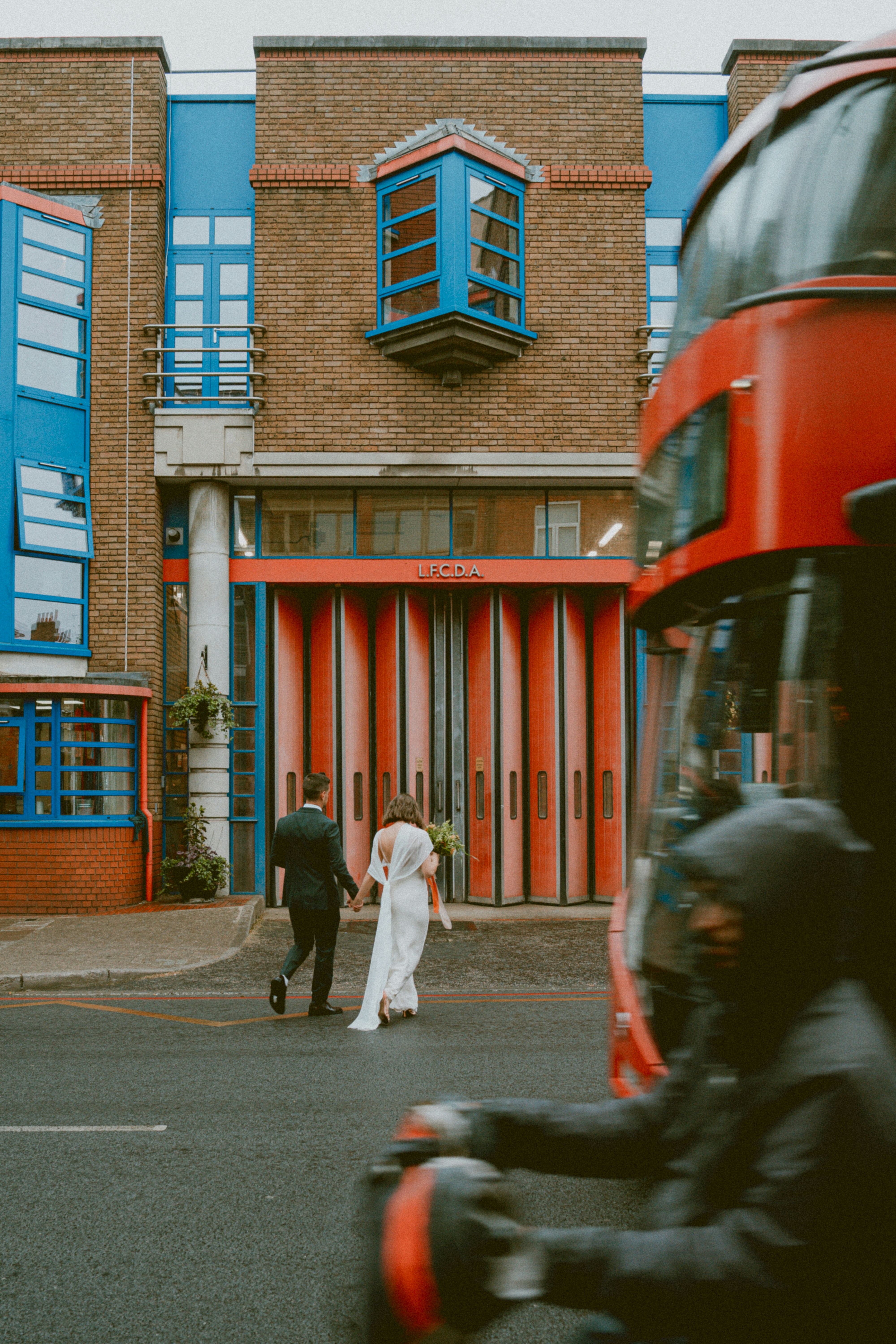 Couple in wedding attire before a vivid red-arched doorway framed by blue storefronts