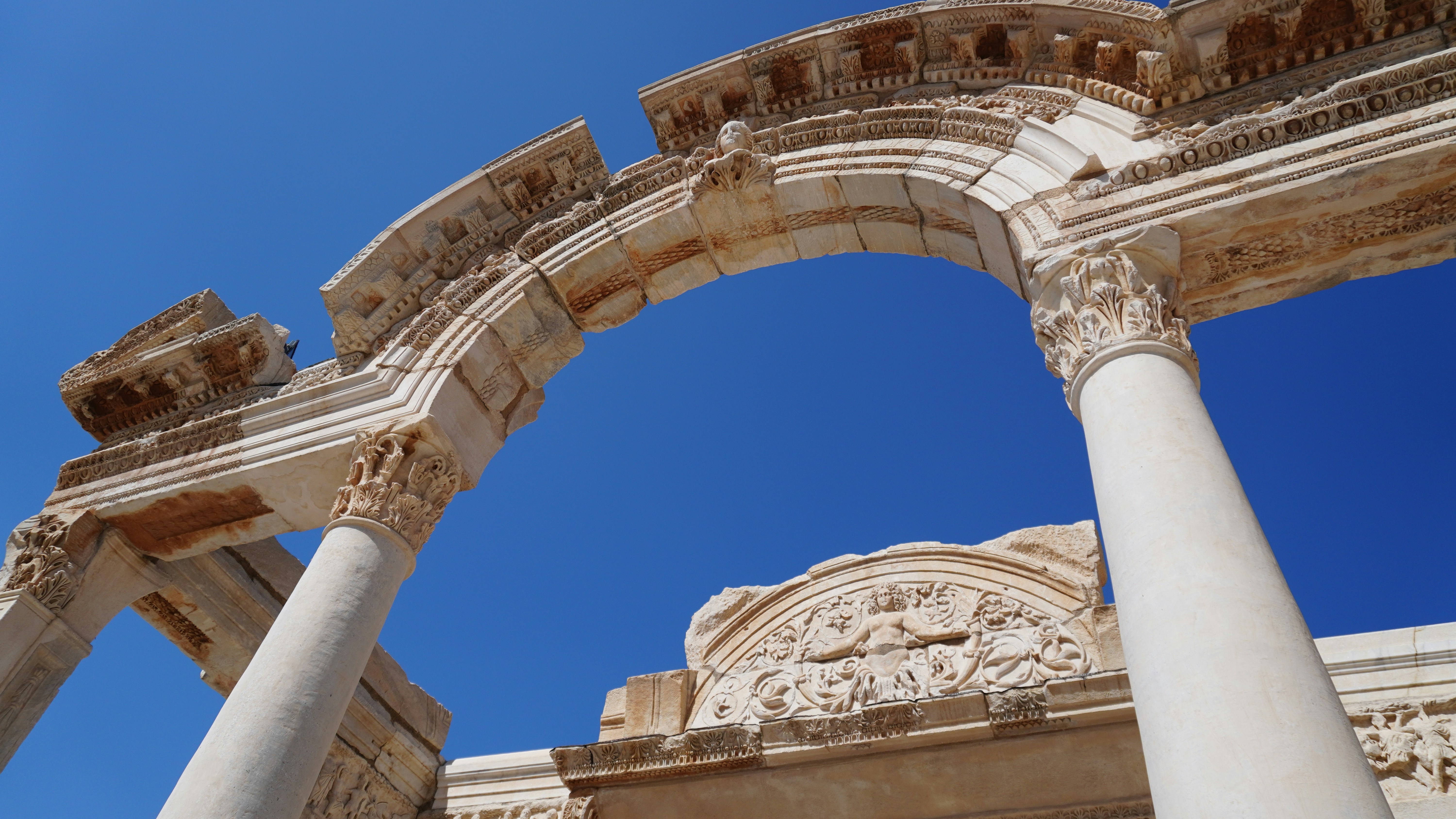 Ancient stone archway with weathered columns against a vivid blue sky, capturing architectural details and carved reliefs.