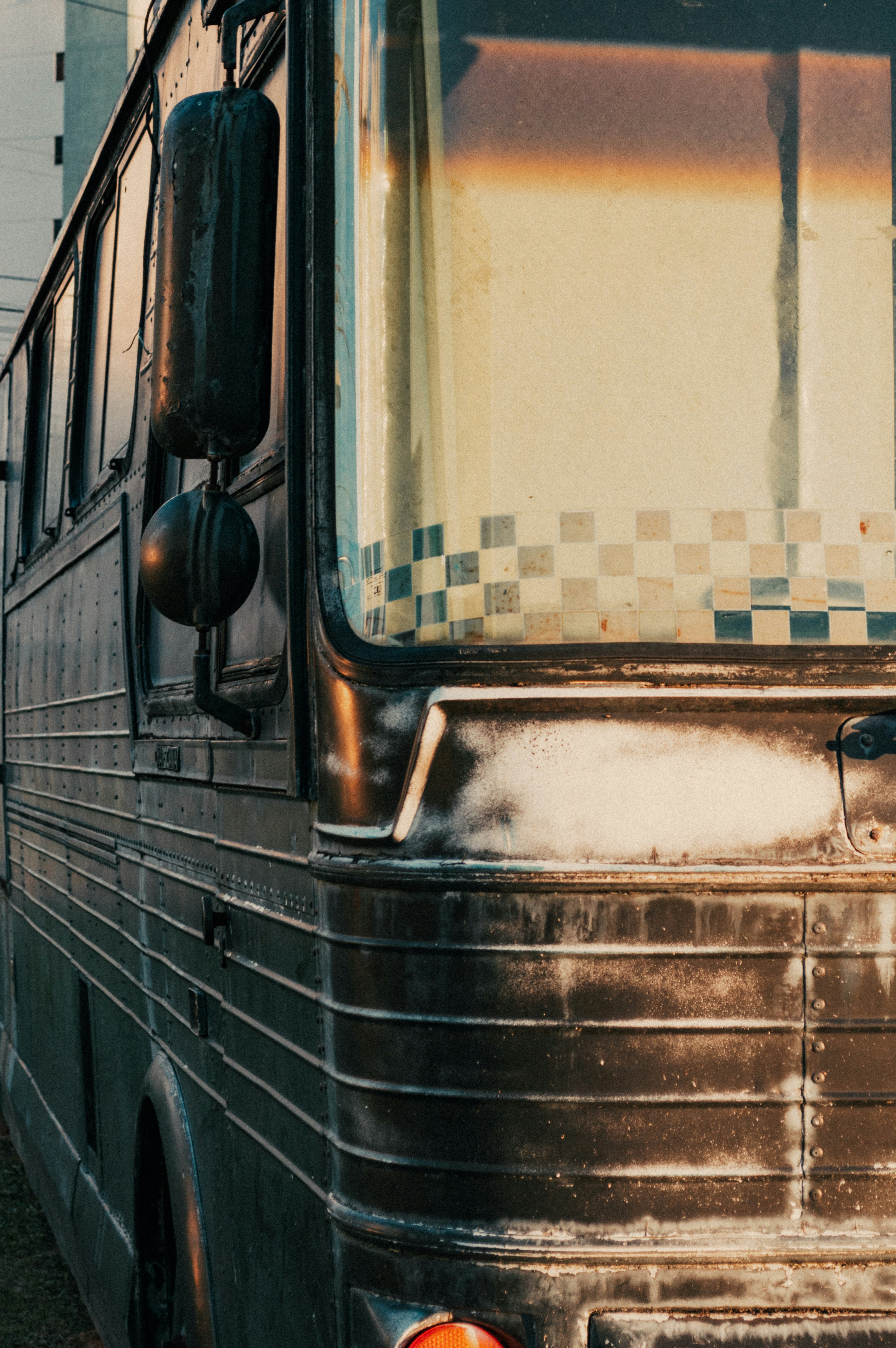Weathered chrome and checkered light: the front of a vintage bus