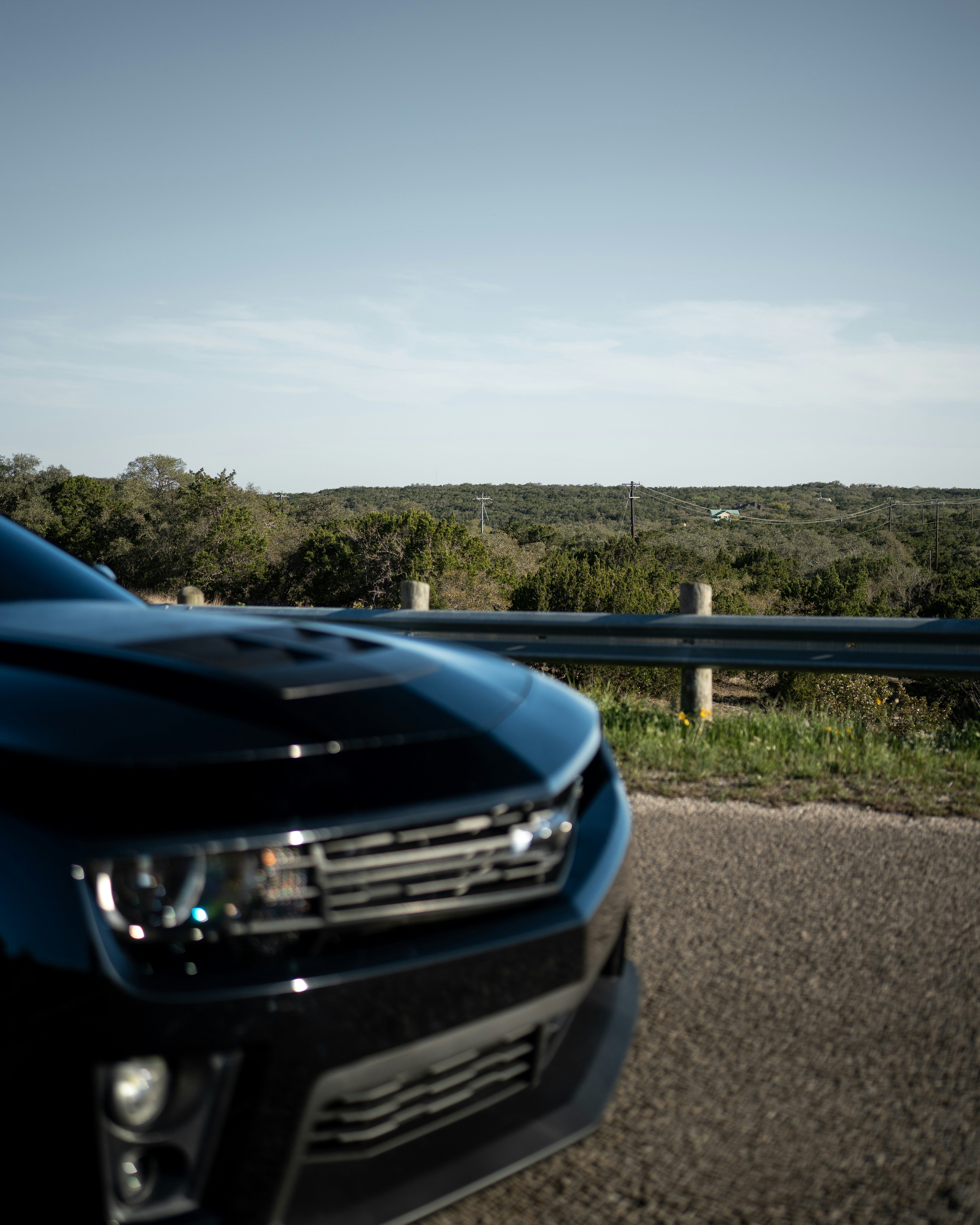 Black car parked roadside with a green, wooded landscape.