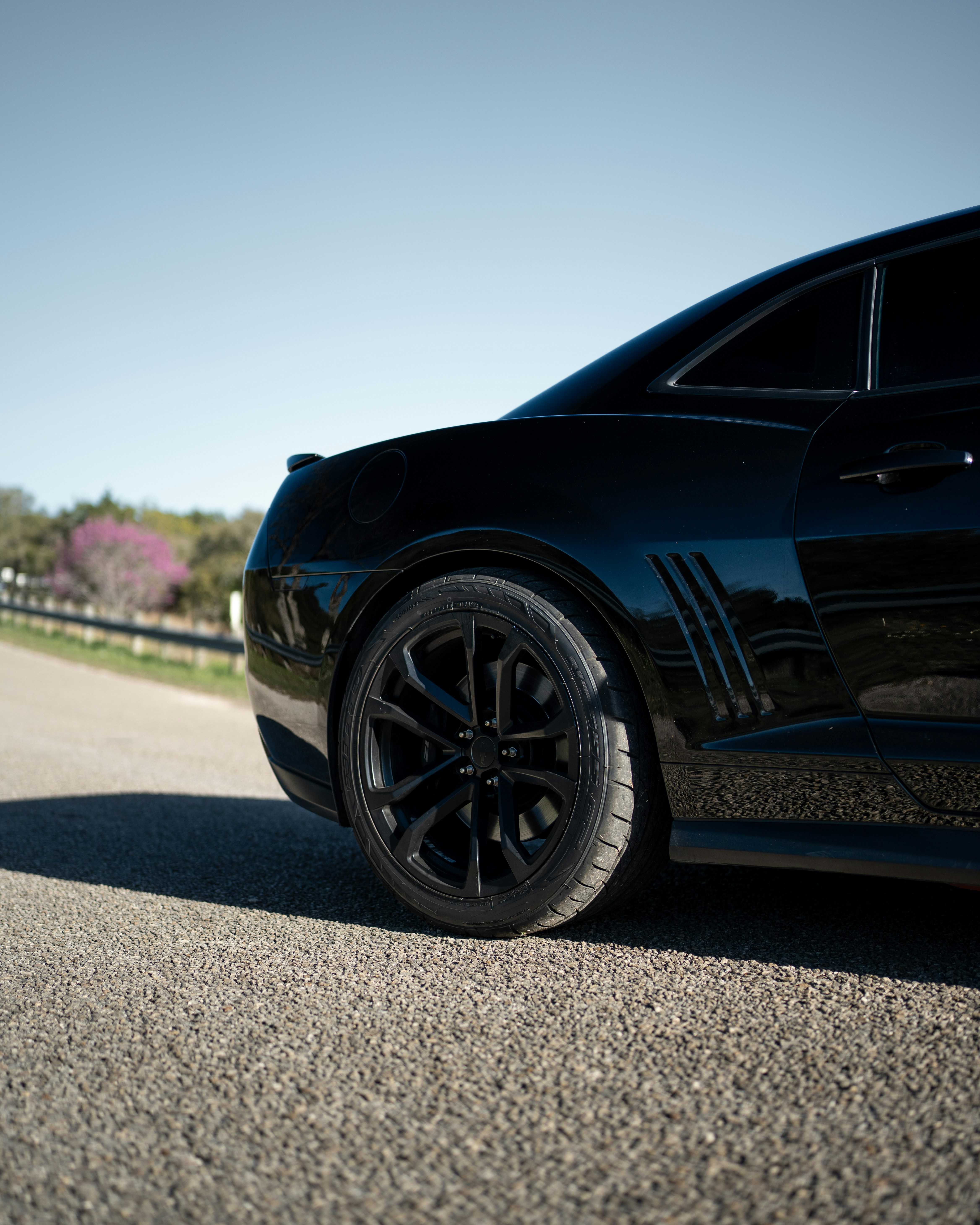 Low-angle roll: black sports sedan and wheel detail under a clear sky