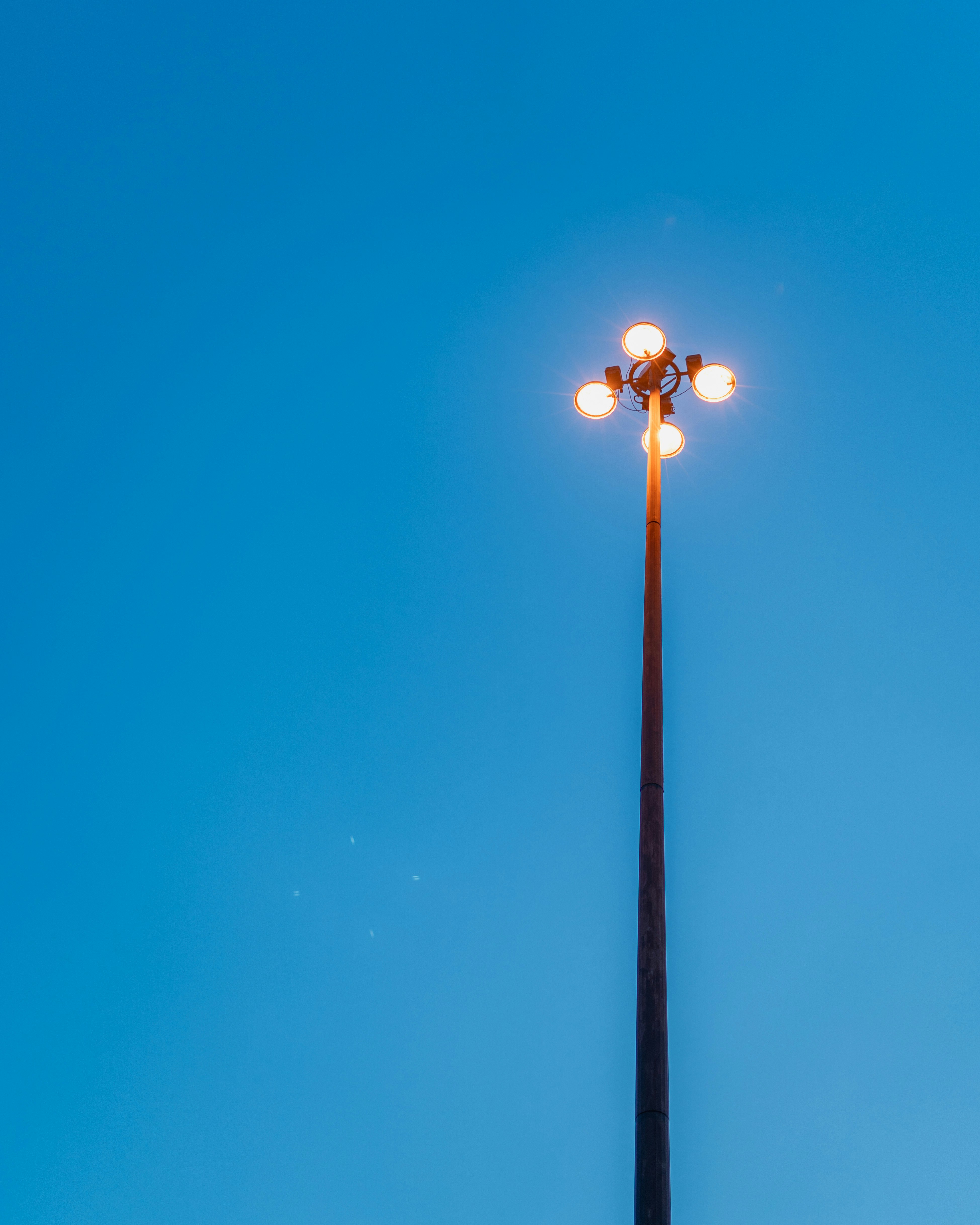 Towering Lights: A Lone Poleilluminated Under a Cerulean Sky