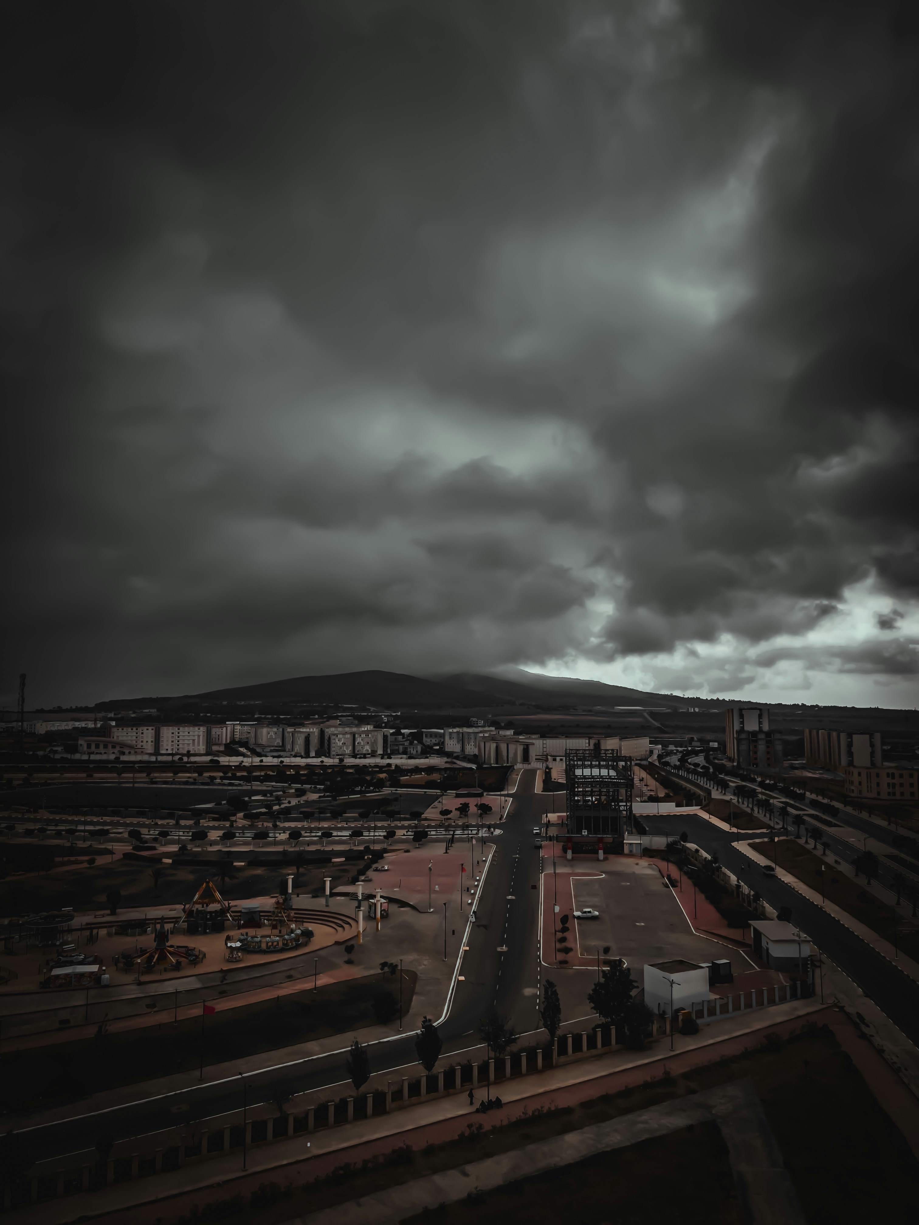 Overcast cityscape with a broad avenue leading toward low hills, subdued reds and grays giving a moody atmosphere; late afternoon geometry captured in a long-shot.