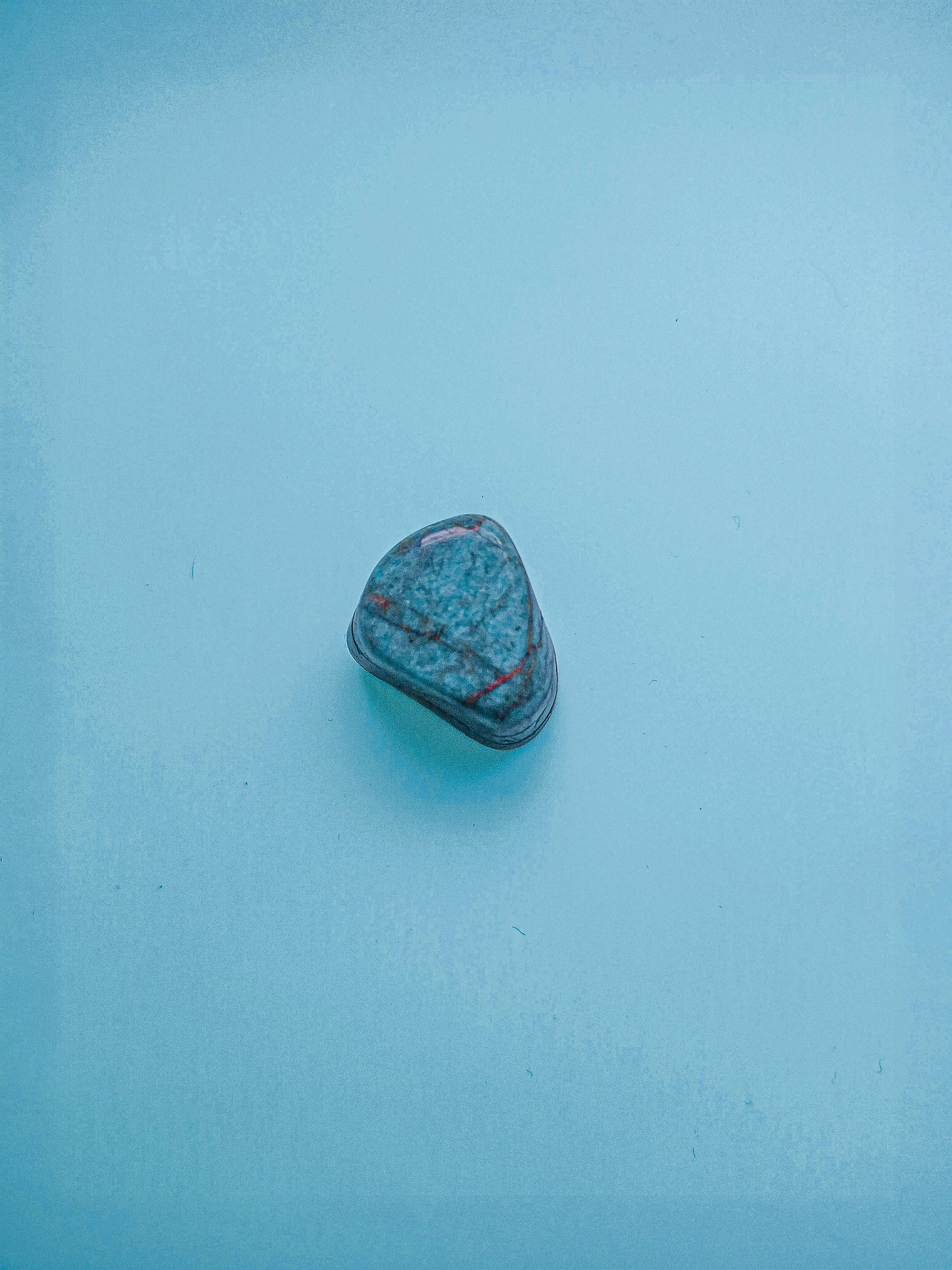 A polished blue-green stone on a solid light blue background.