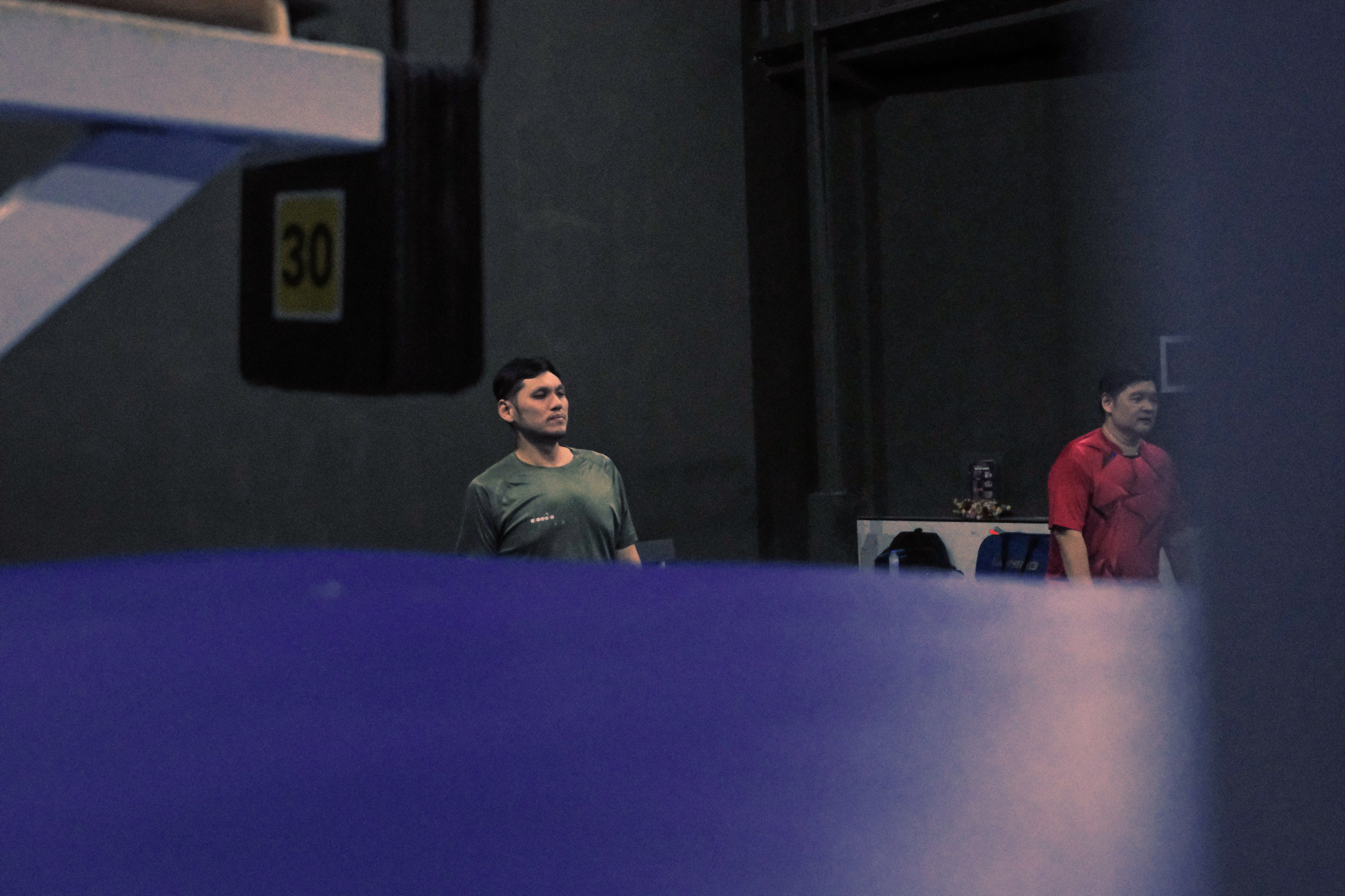 Two Players Stand Guard by an Indoor Court with Deep Blue Barriers