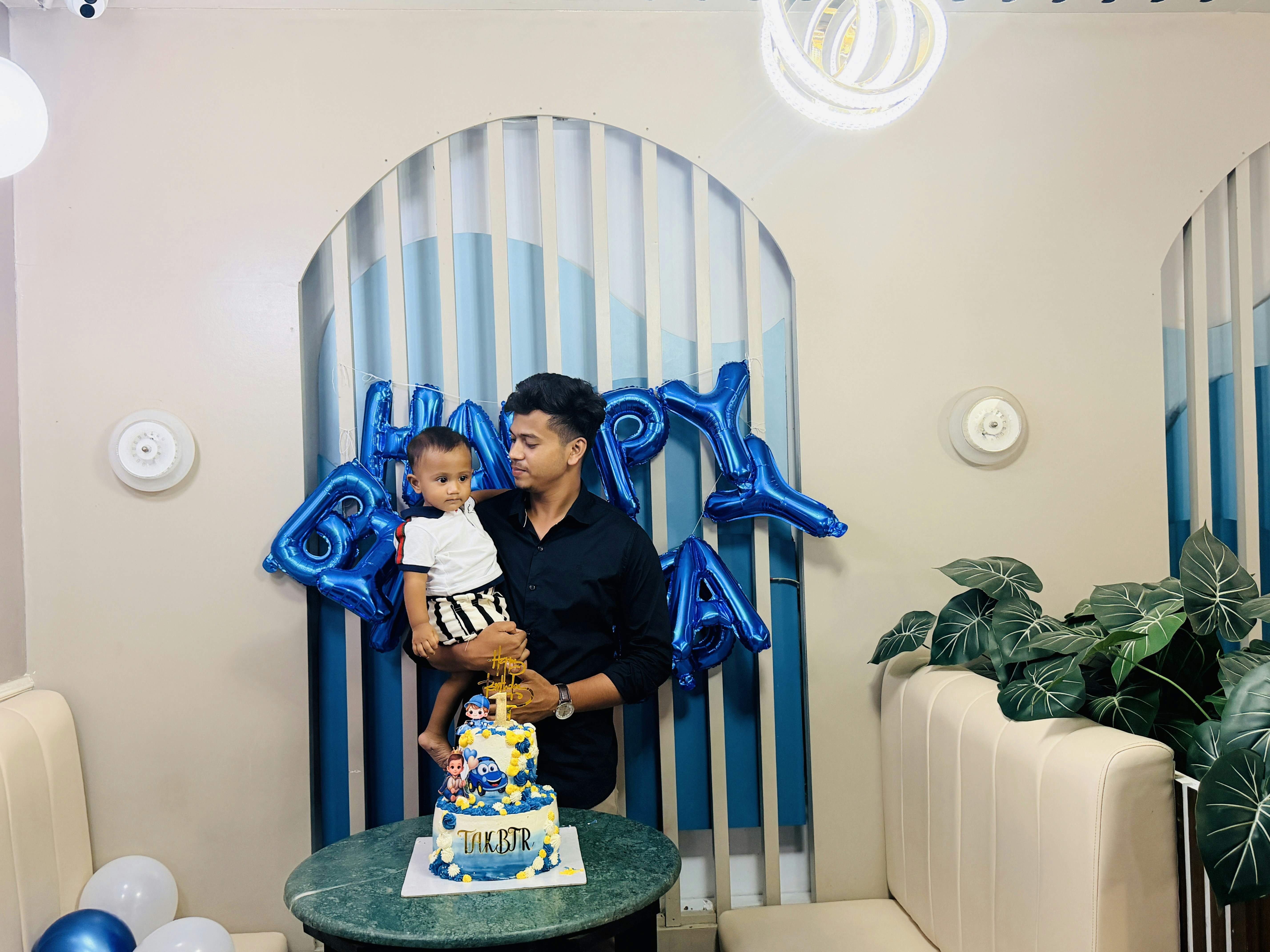 Birthday Moments: A Father and Child Celebrate with a Cake Under Balloon Arch