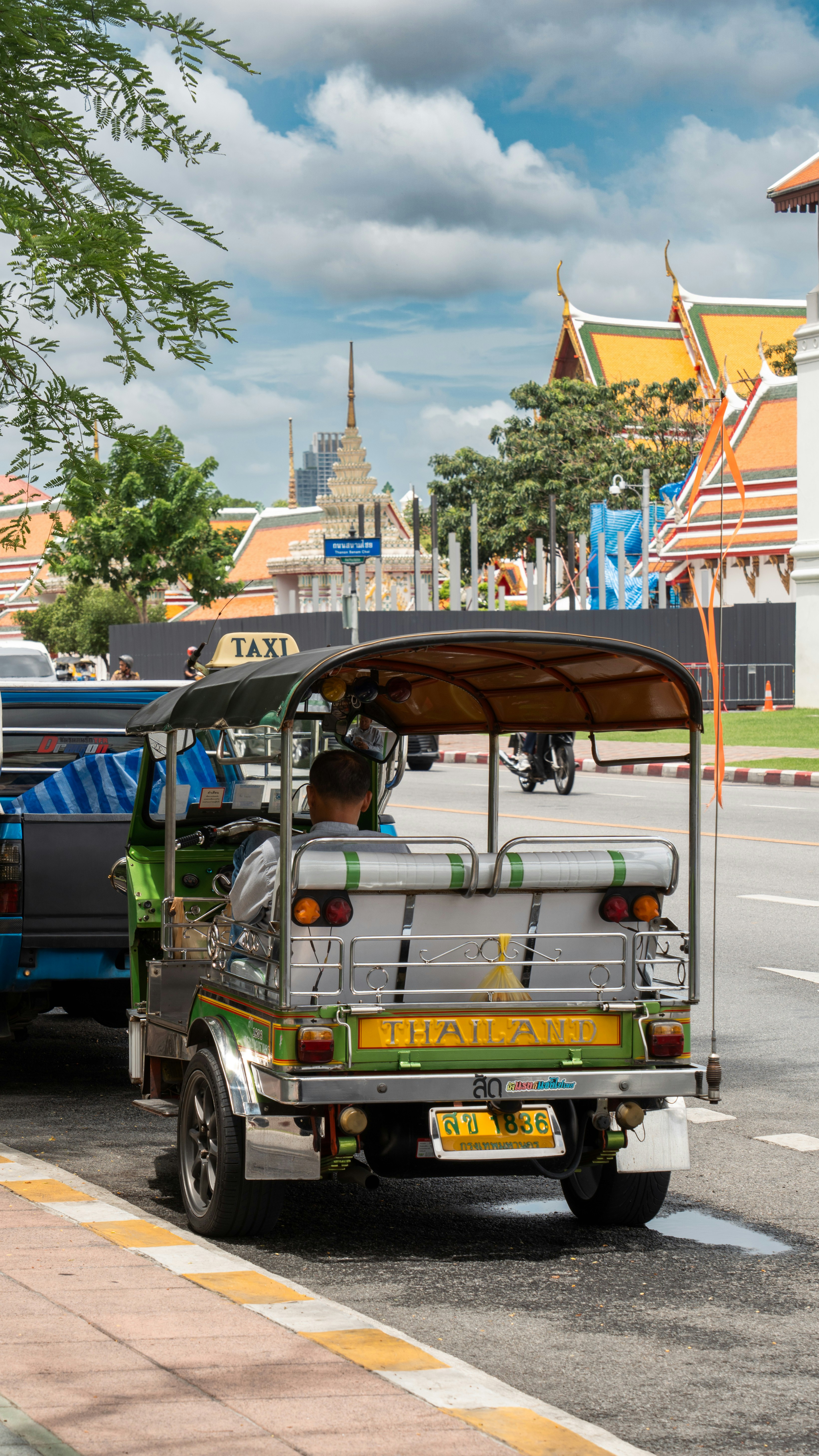A colorful tuk-tuk parked near traditional thai temple buildings.