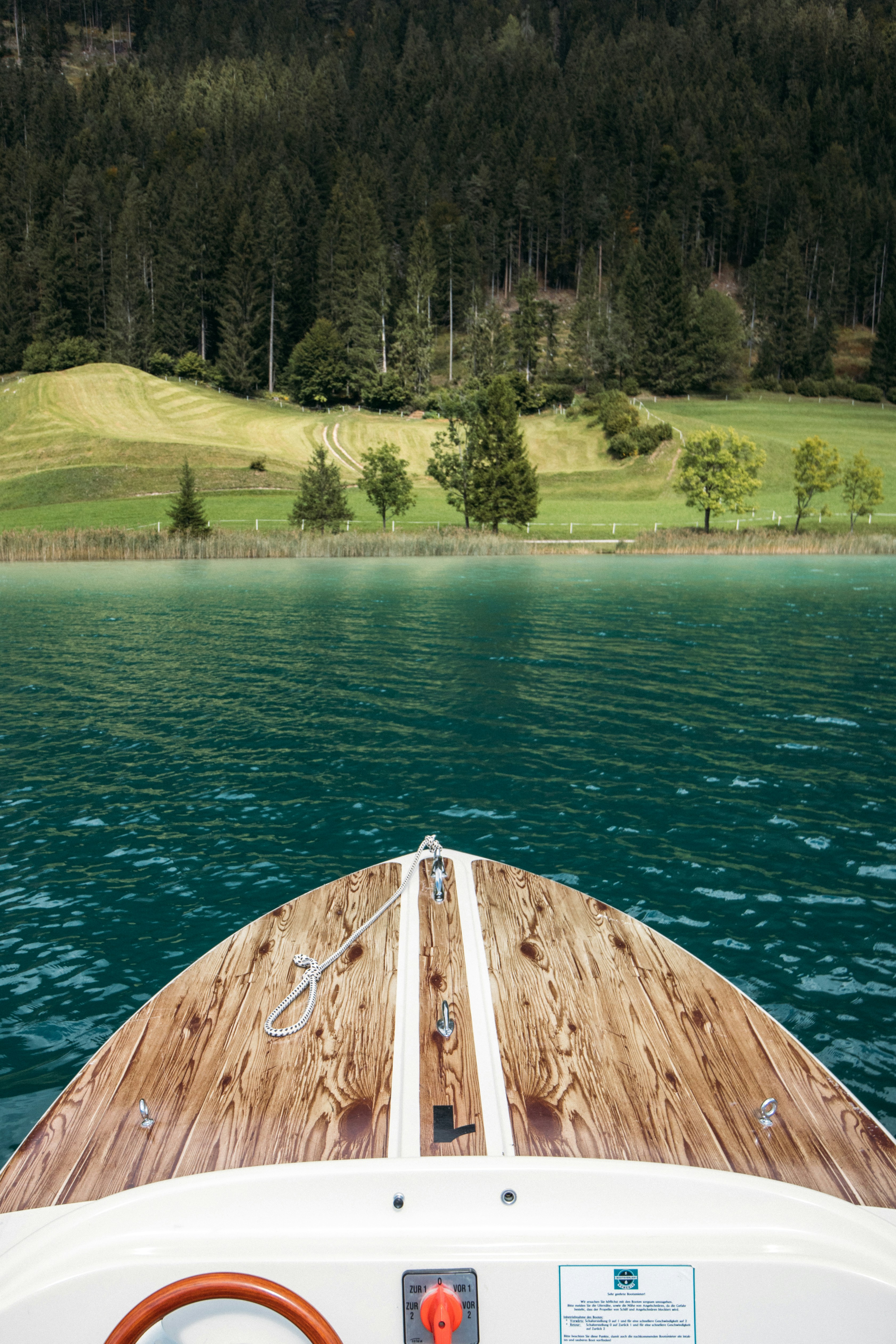 Bow of a sunlit boat cutting across emerald waters toward a forested shoreline
