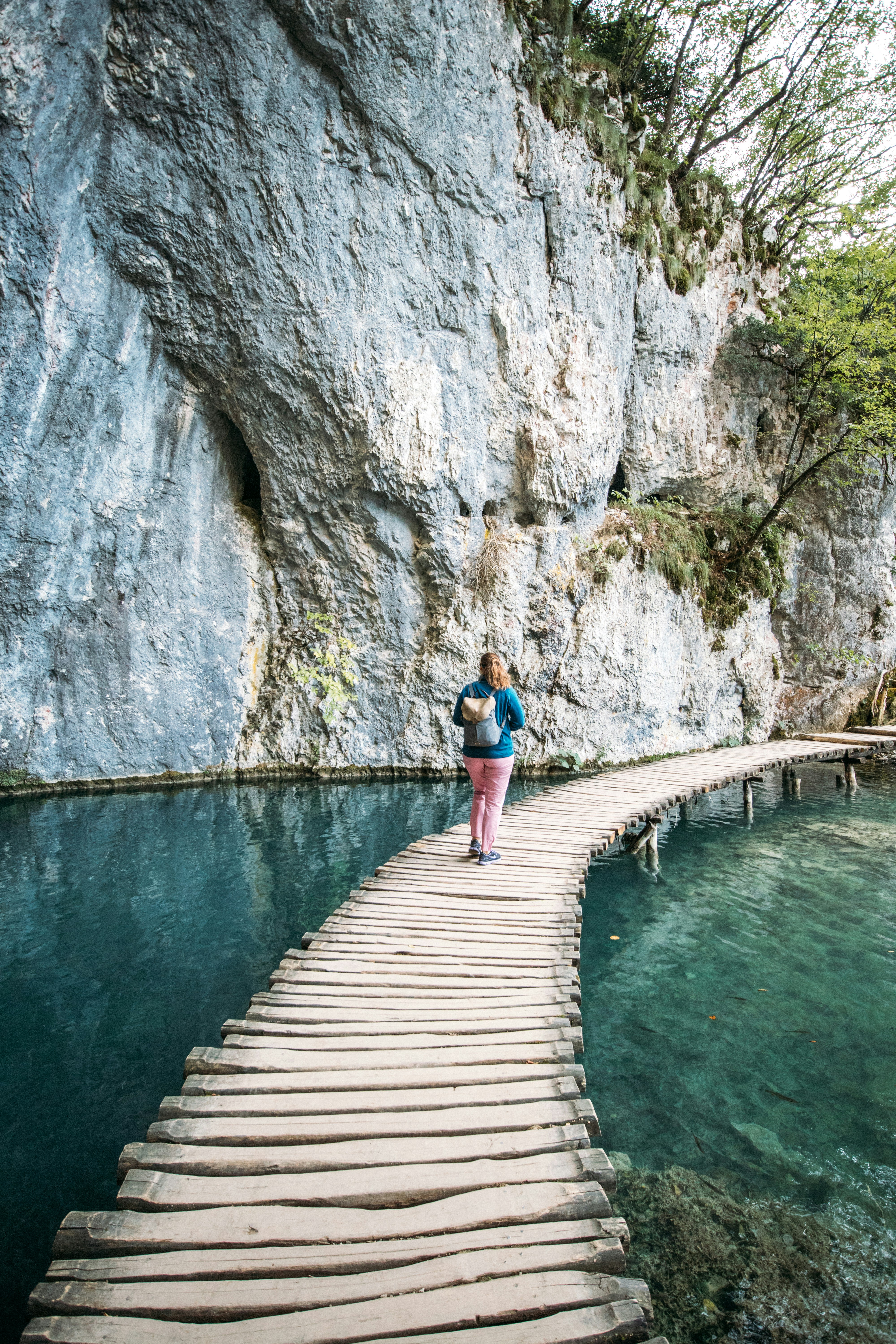 Traveler on a wooden bridge across turquoise waters beside a limestone cliff