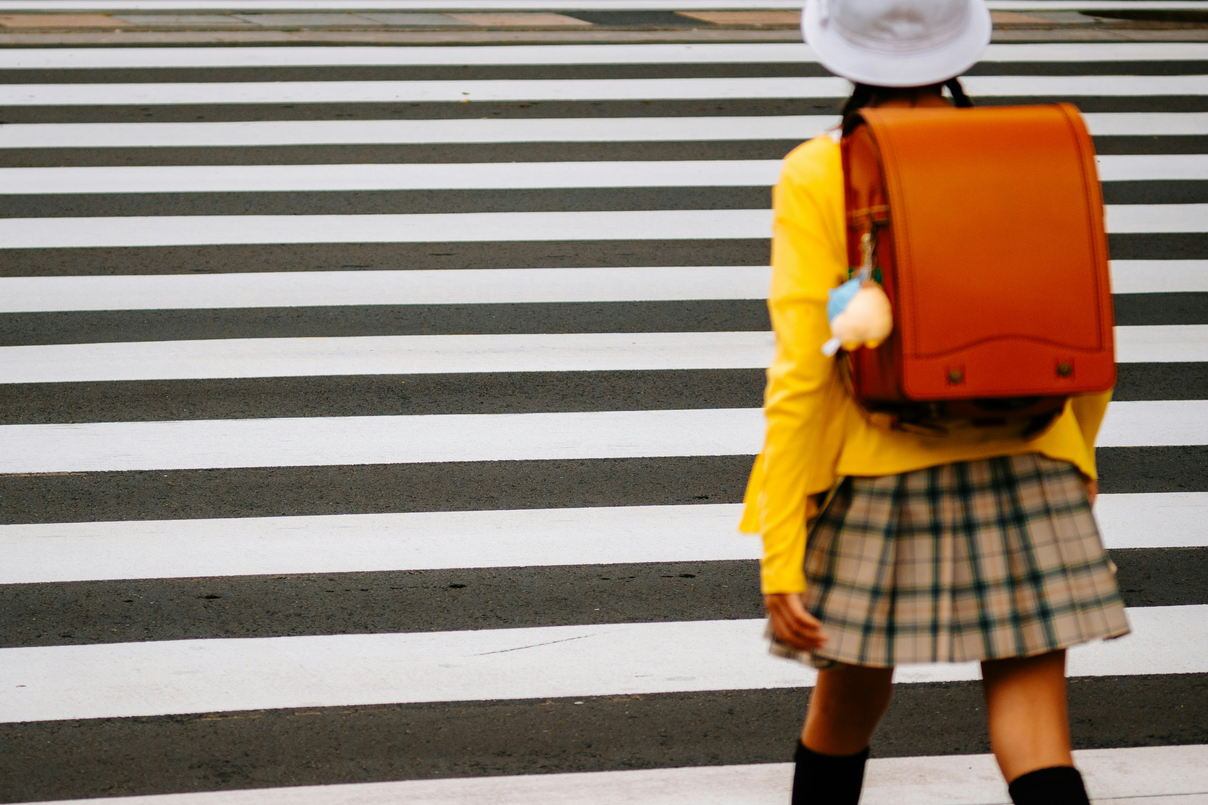 Orange backpack crossing: a schoolgirl steps into the striped street